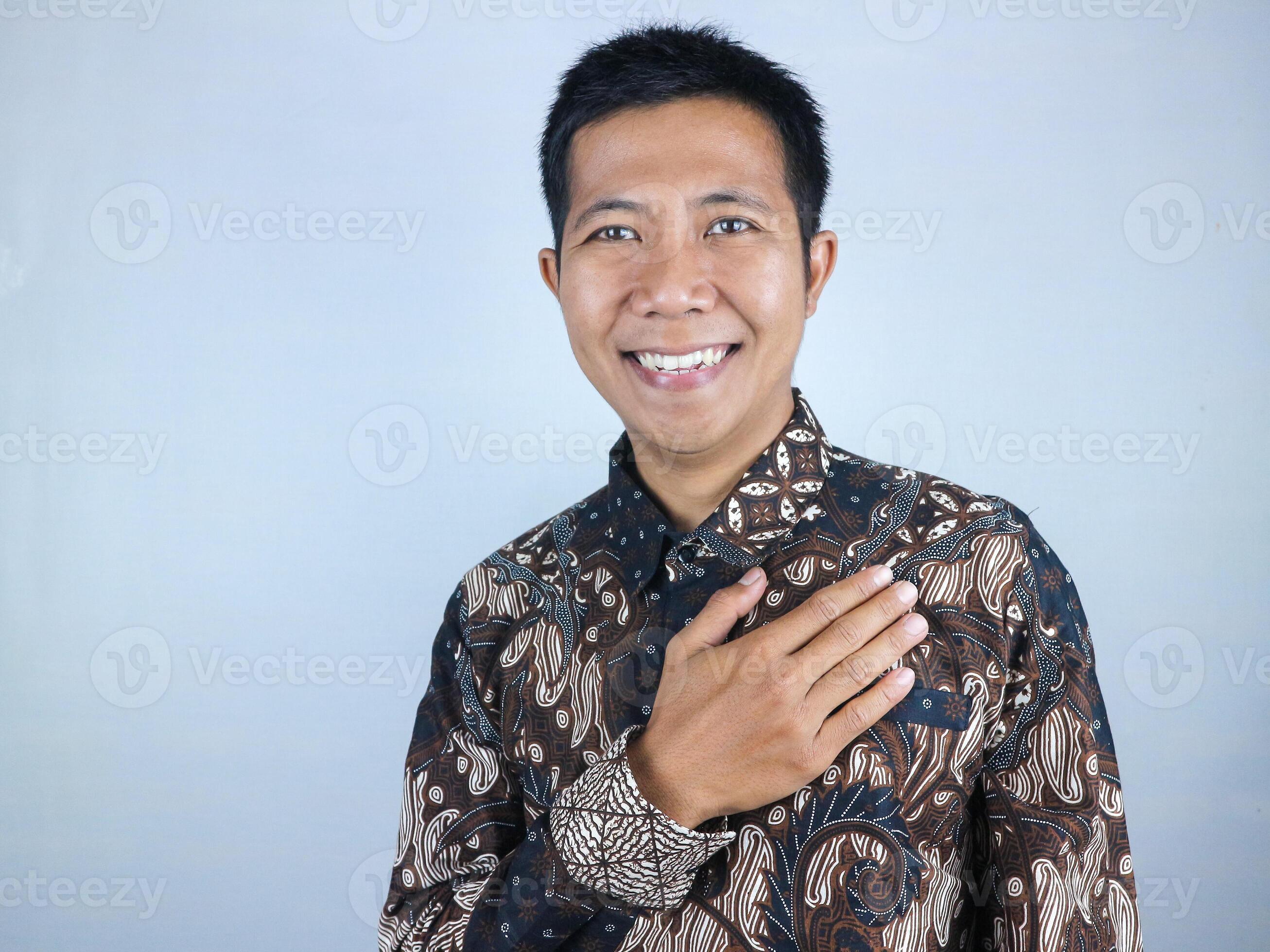 Smiling face expression of asian man wearing batik while hand on chest ...