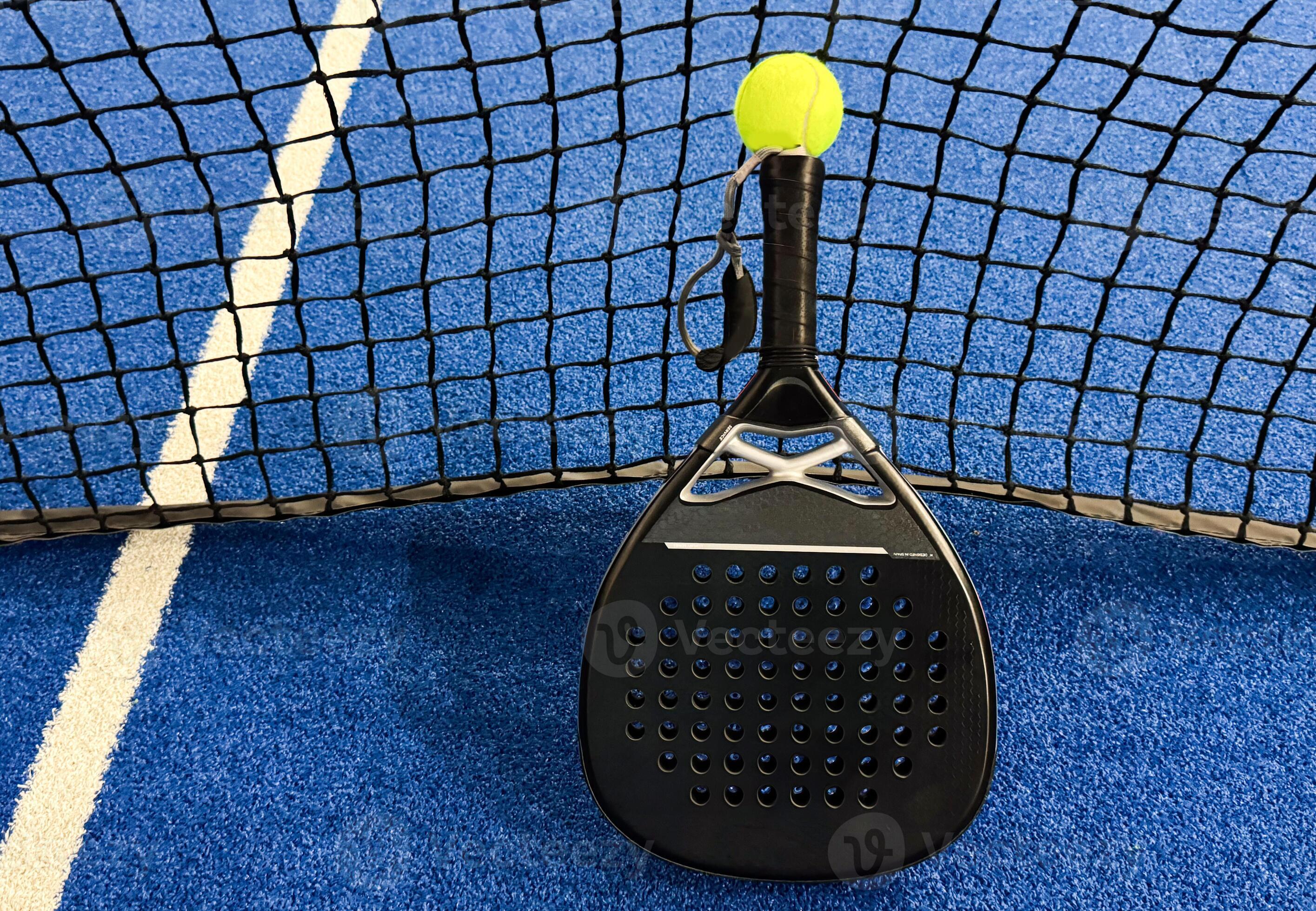 Yellow ball on floor behind paddle net in blue court outdoors. Padel tennis is a racquet game ...