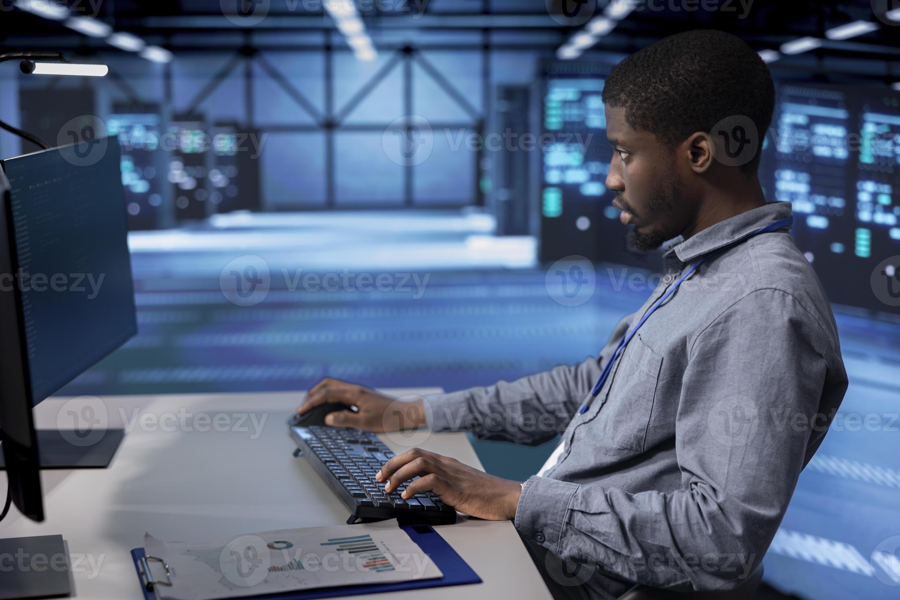 African american man typing on PC in server farm, ensuring data remains shielded from potential ...