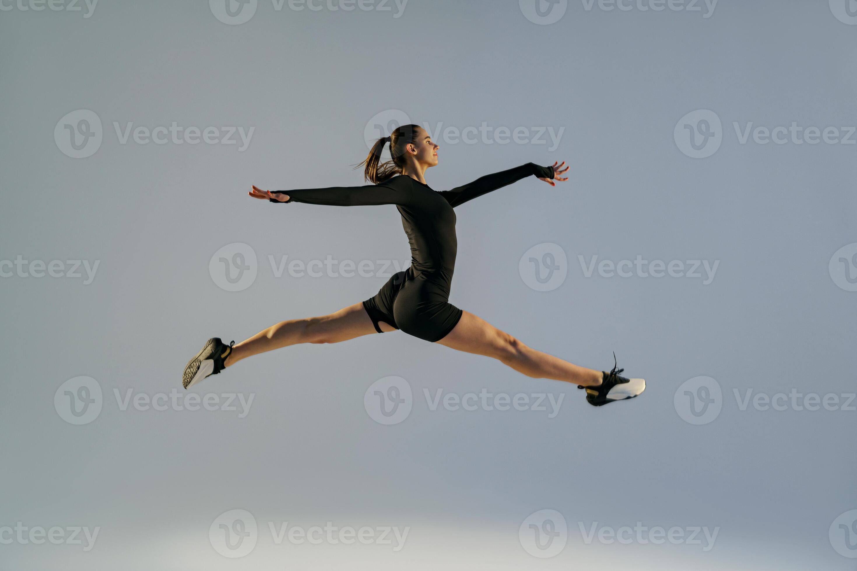 Sporty girl jumping doing split leap in air with joyful expression. Flexible and weightless ...