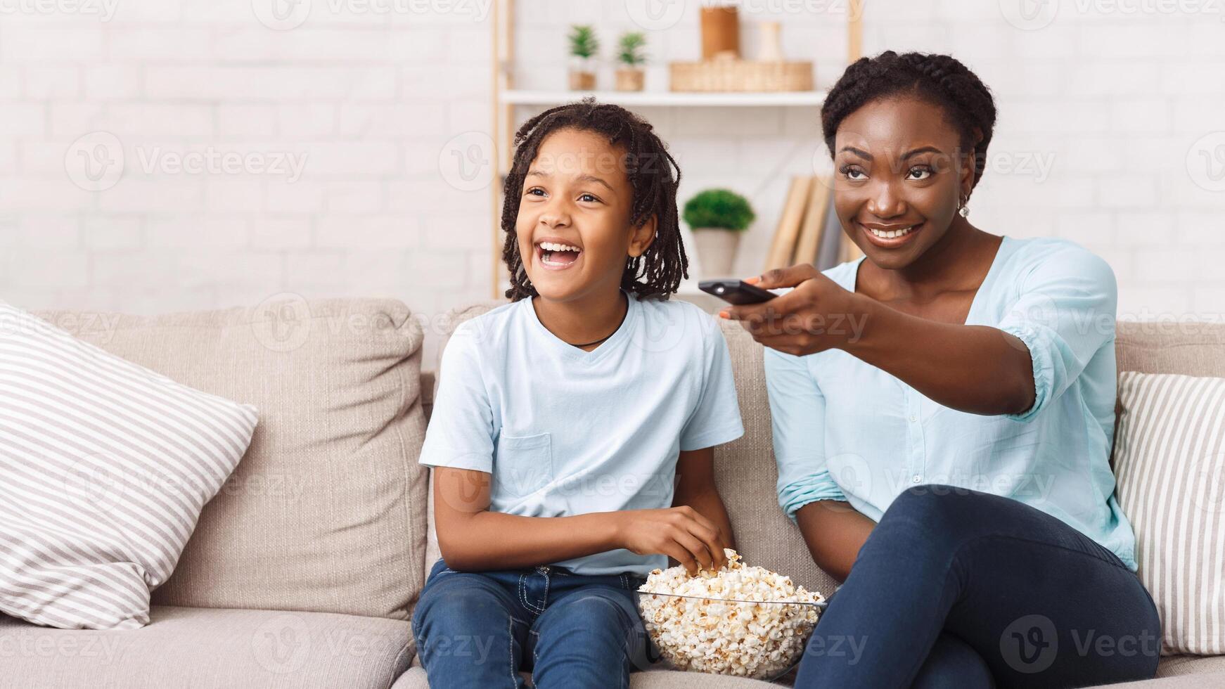 Mother With Daughter. Happy black family watching tv movie, cartoons or football with popcorn ...