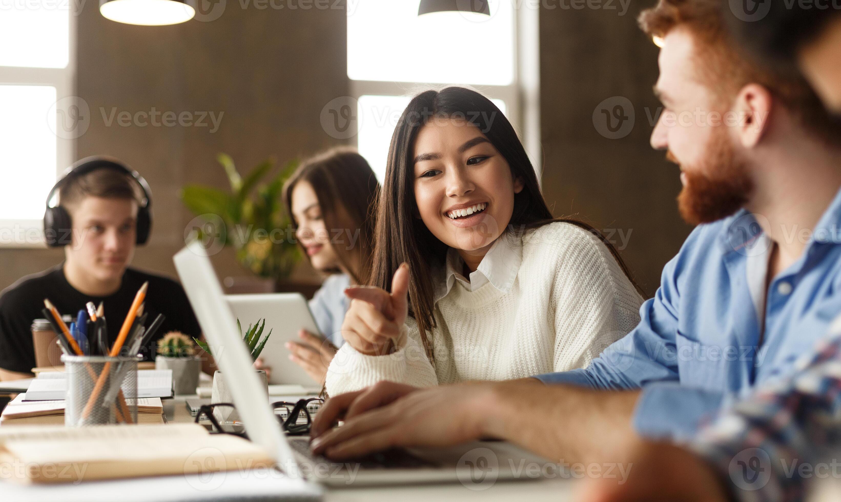 College students using laptop in library, studying for school assignment, discussing together ...