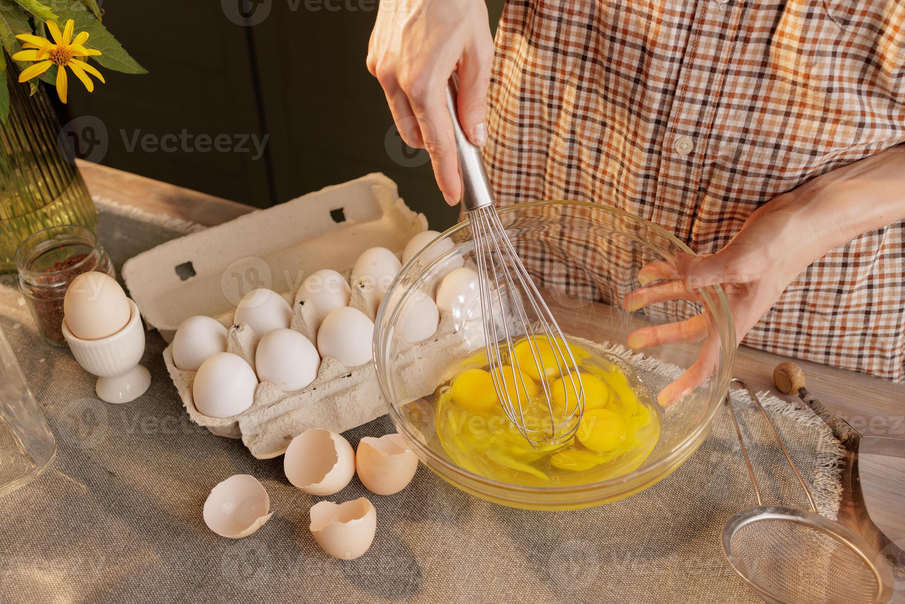 Close-up of female hands beating eggs with a hand whisk in a transparent bowl against 51417815 ...
