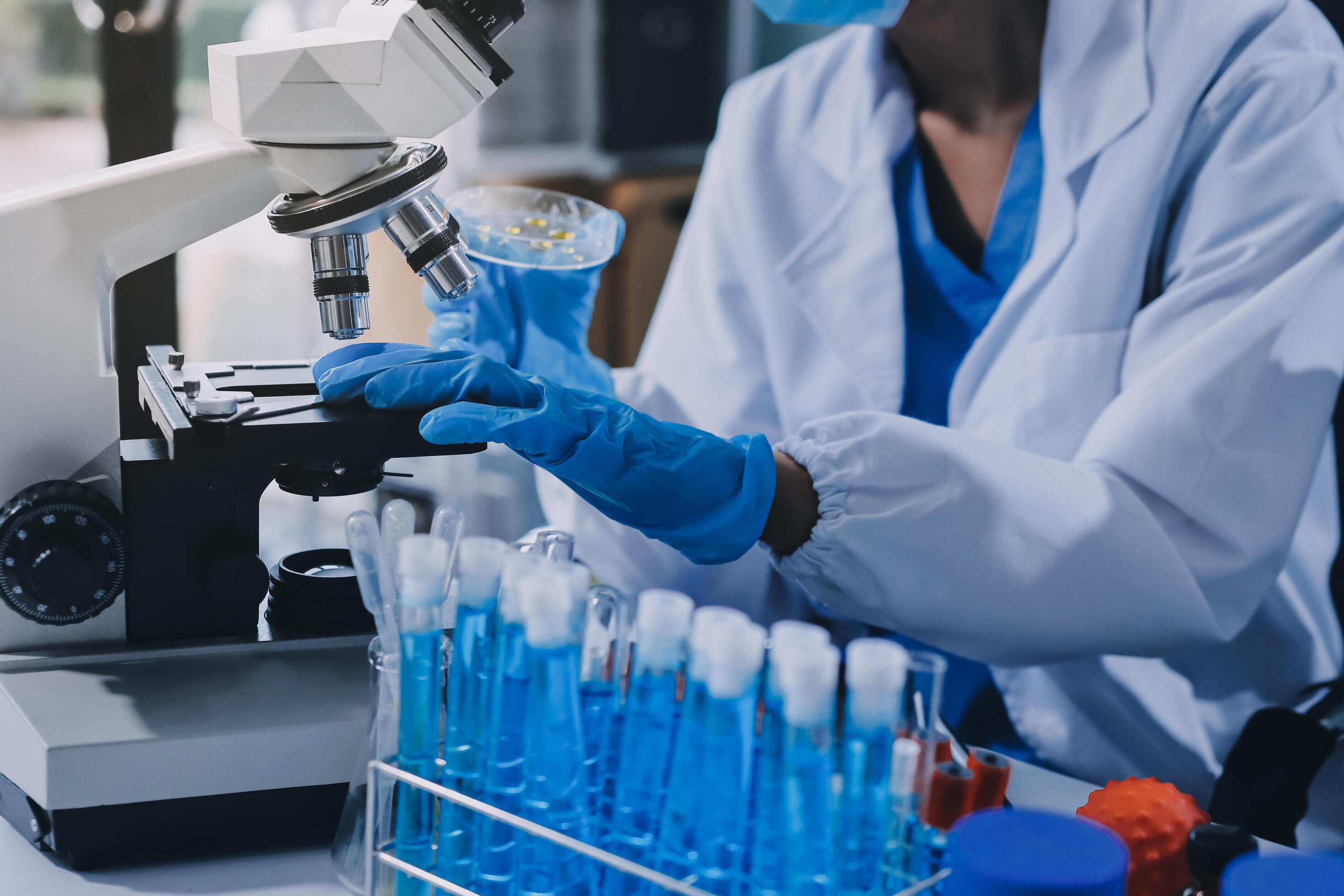 Scientist using microscope in laboratory. Close-up of a researcher's hands adjusting a modern ...