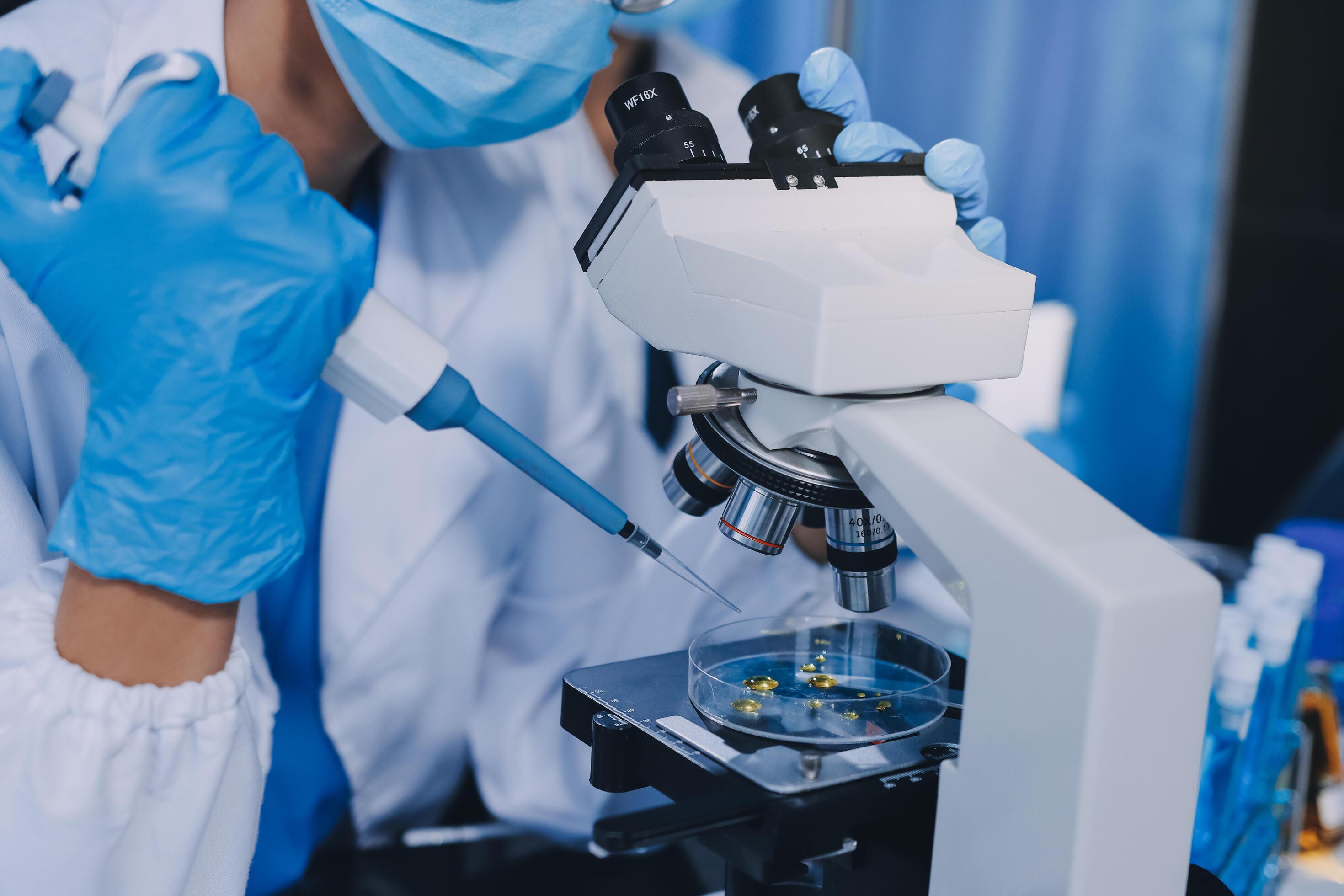 Scientist using microscope in laboratory. Close-up of a researcher's hands adjusting a modern ...