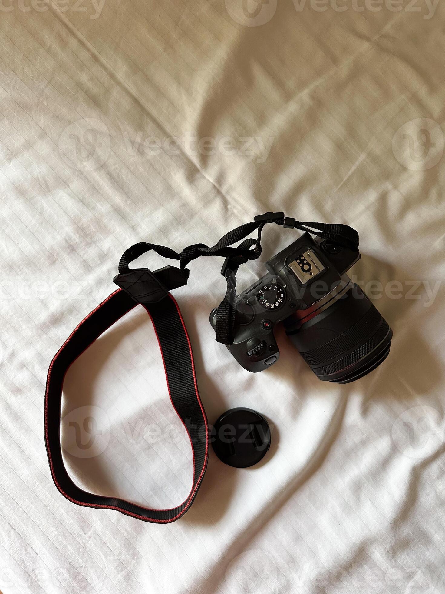 Camera with a strap placed on a white bed sheet, capturing the essence of travel preparation and ...