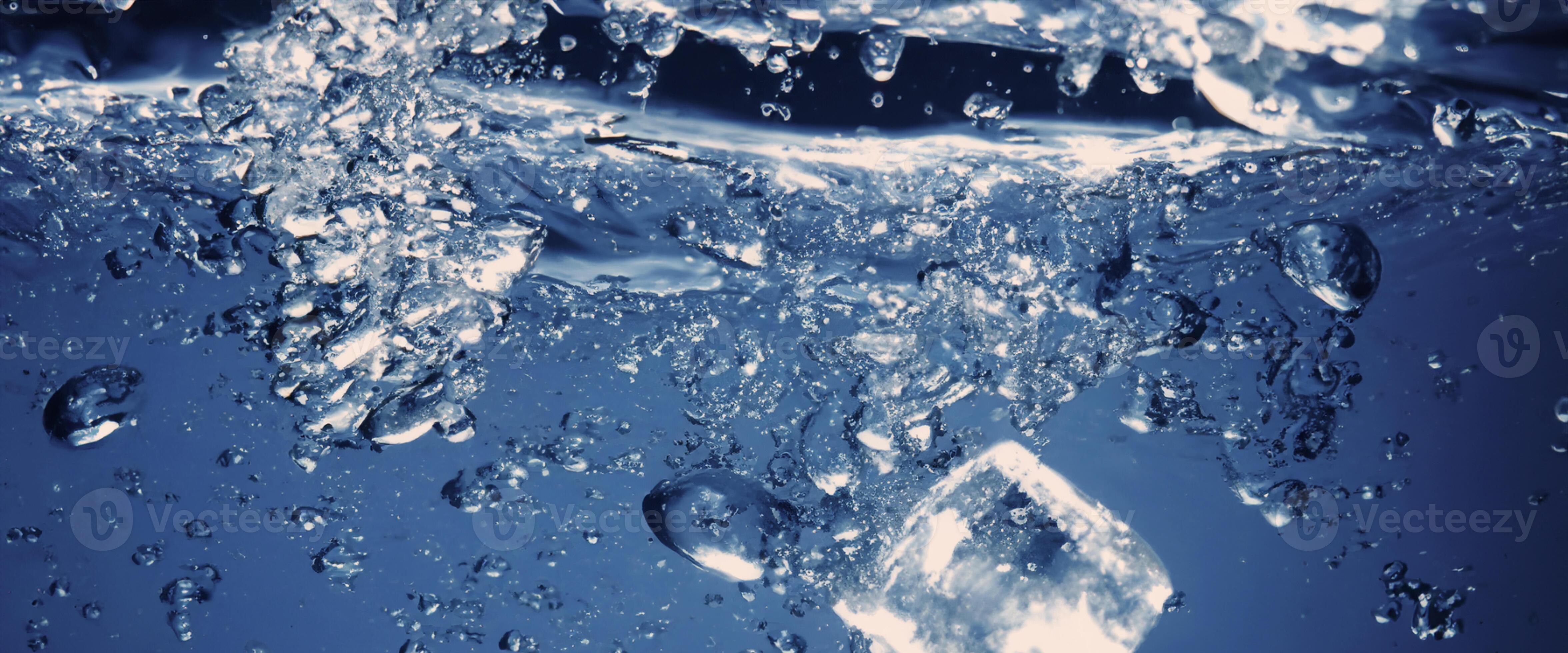 Water splashing and ice cube. Ice splashing into a glass of water. Underwater pouring ice cubes ...