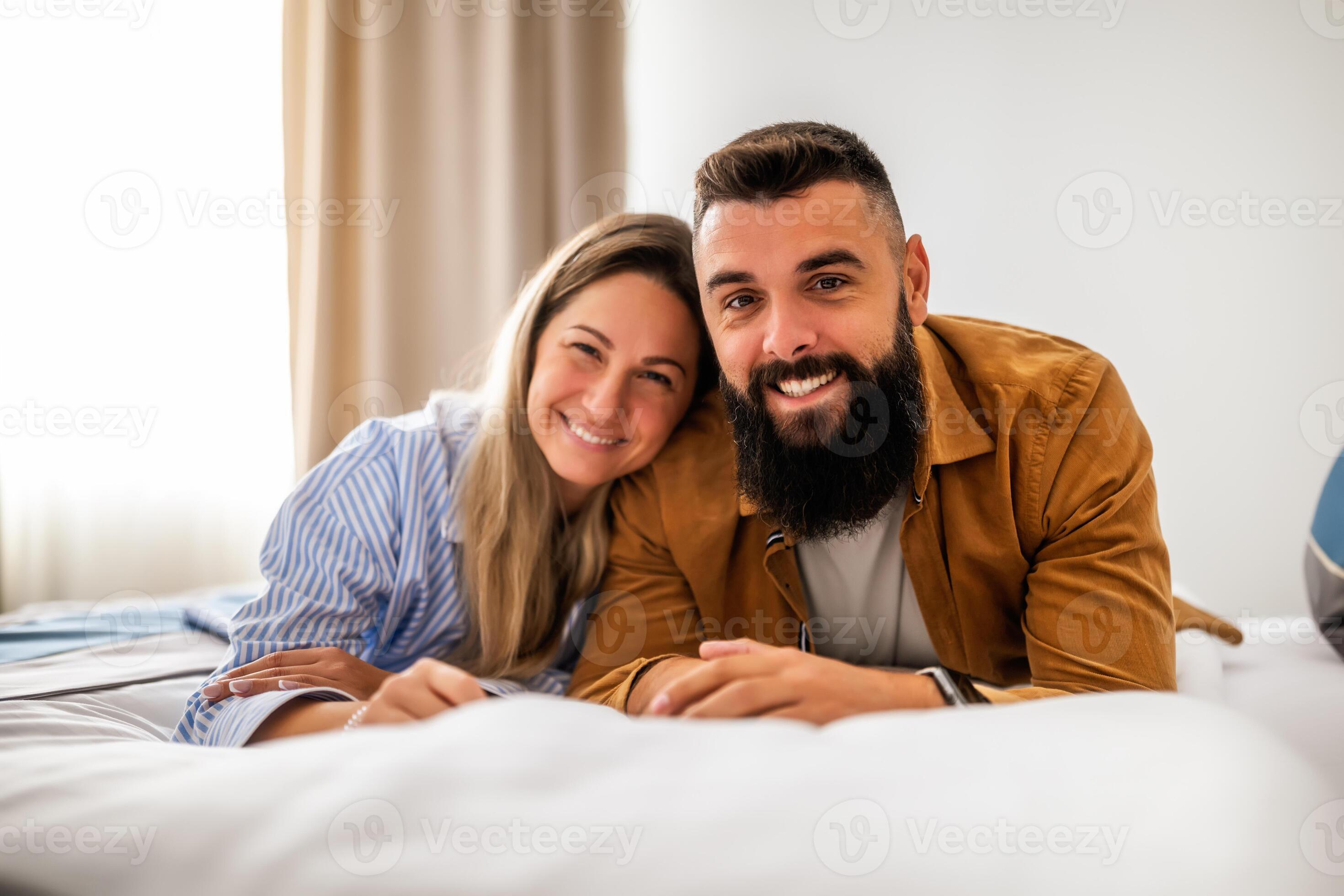 Young happy couple is lying on bed in their bedroom, looking at camera and smiling. 53093499 ...