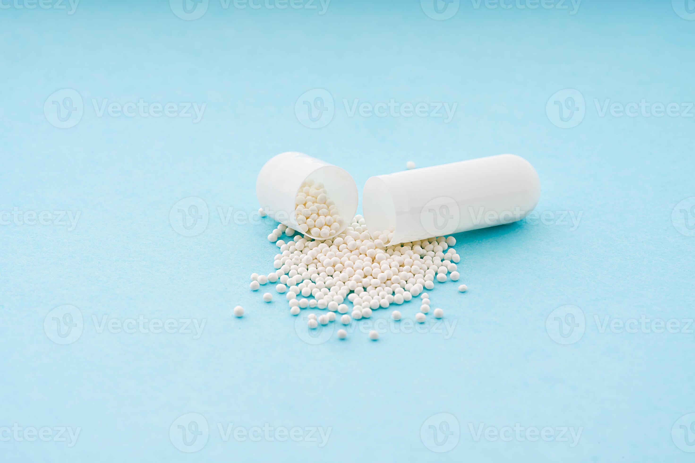 Gel capsule opened. White medicine powder spilled out on light blue background from capsule drug ...