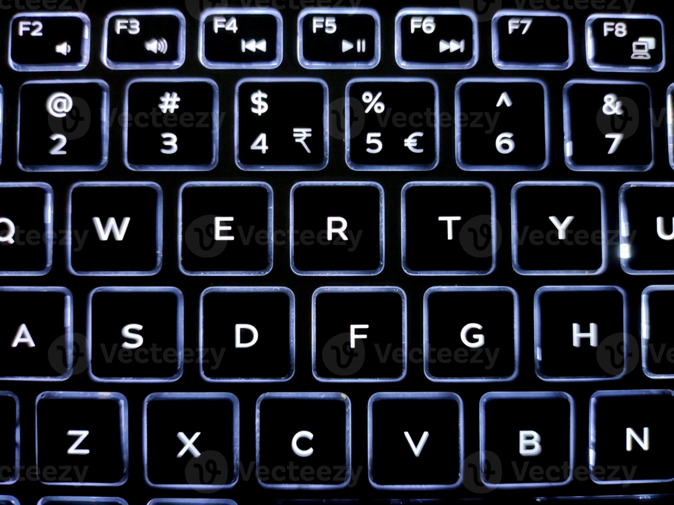 A close-up of a backlit keyboard with illuminated keys in a QWERTY layout. White letters on ...