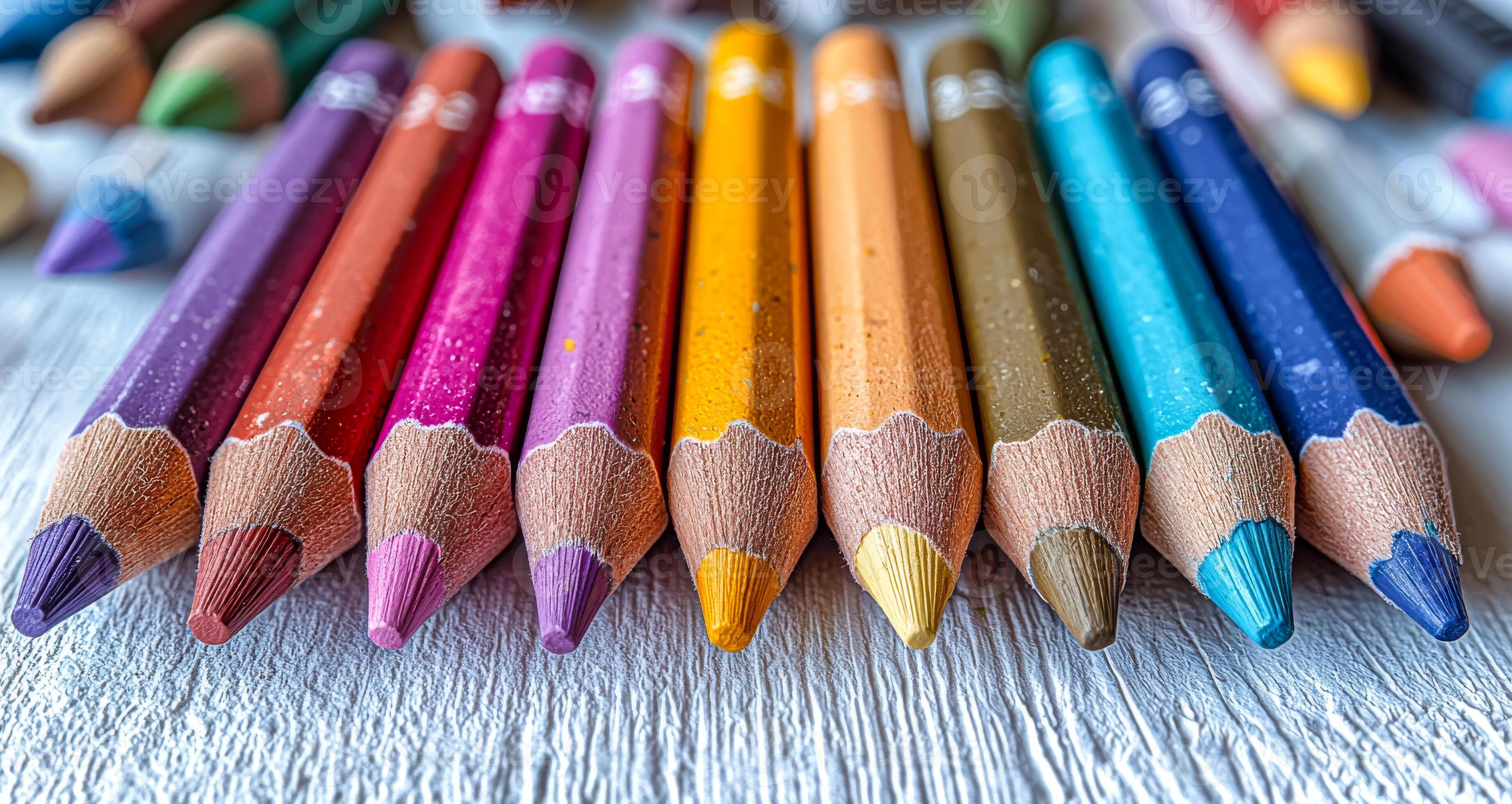 A row of colored pencils are lined up on a table. The pencils are of different colors and sizes ...