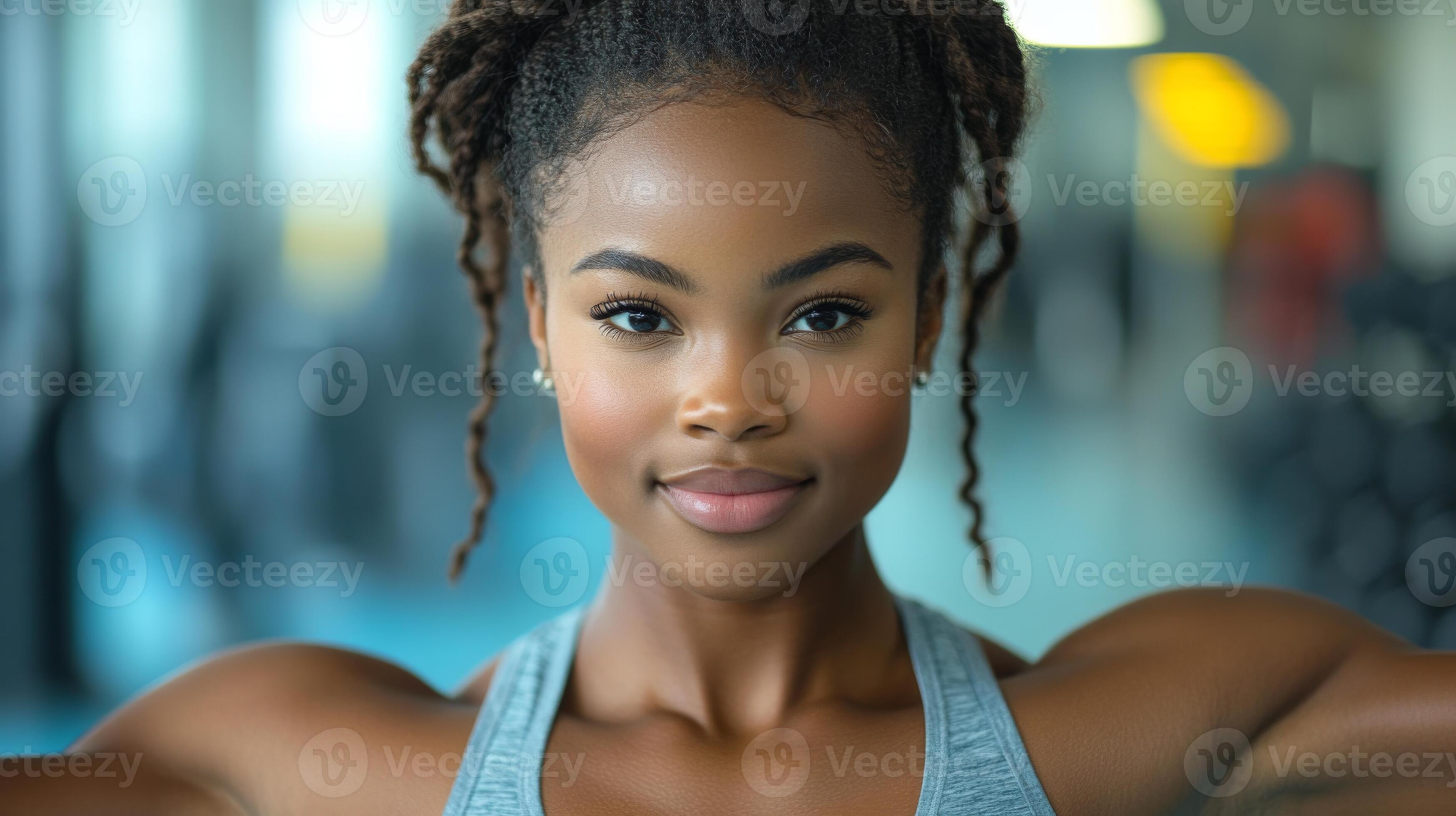 A young woman showcases her muscular arms while smiling confidently in a well-equipped gym. The ...