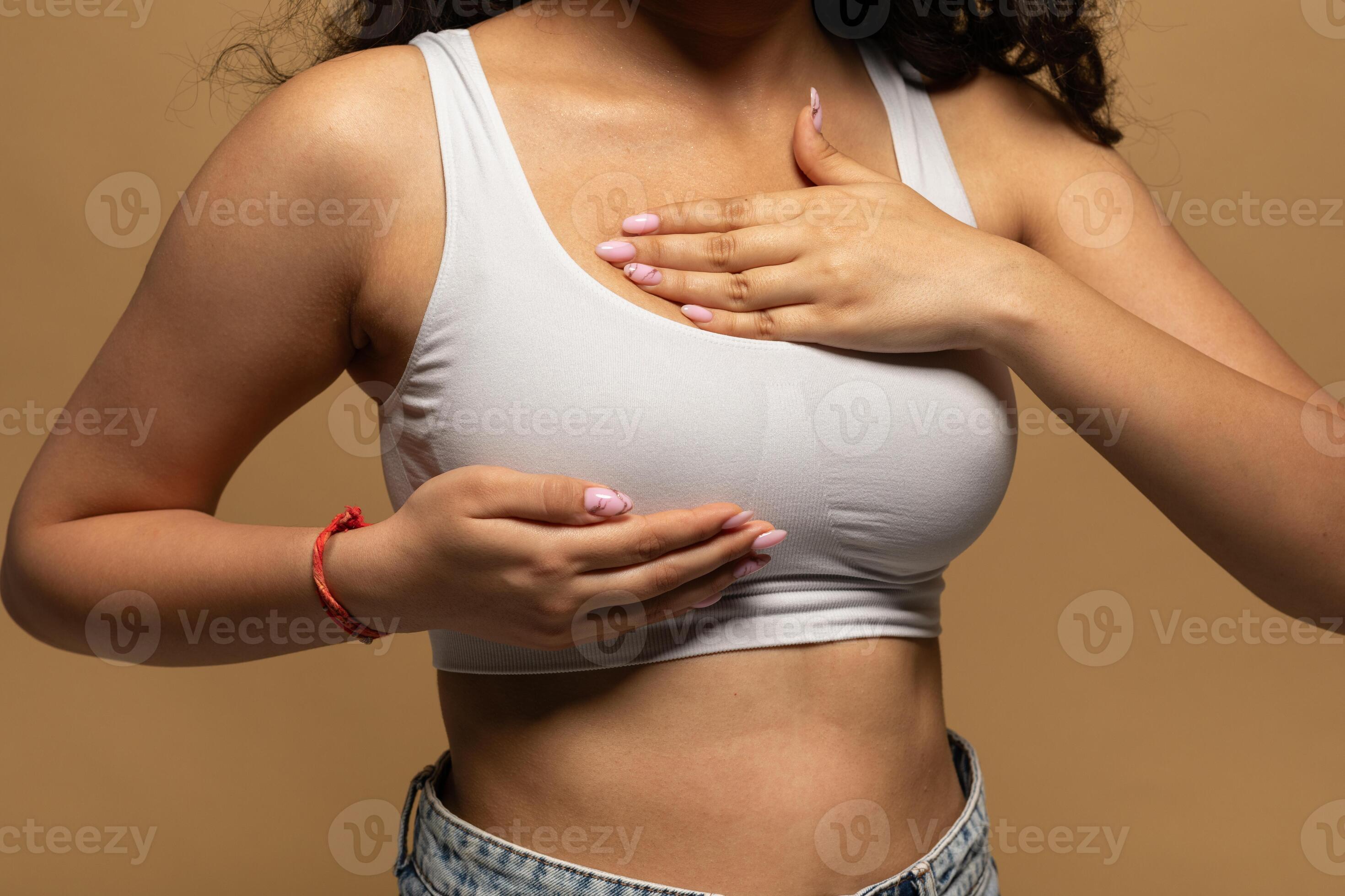 Young woman touching her breast, checking for cancer signs, cropped, isolated on beige studio ...