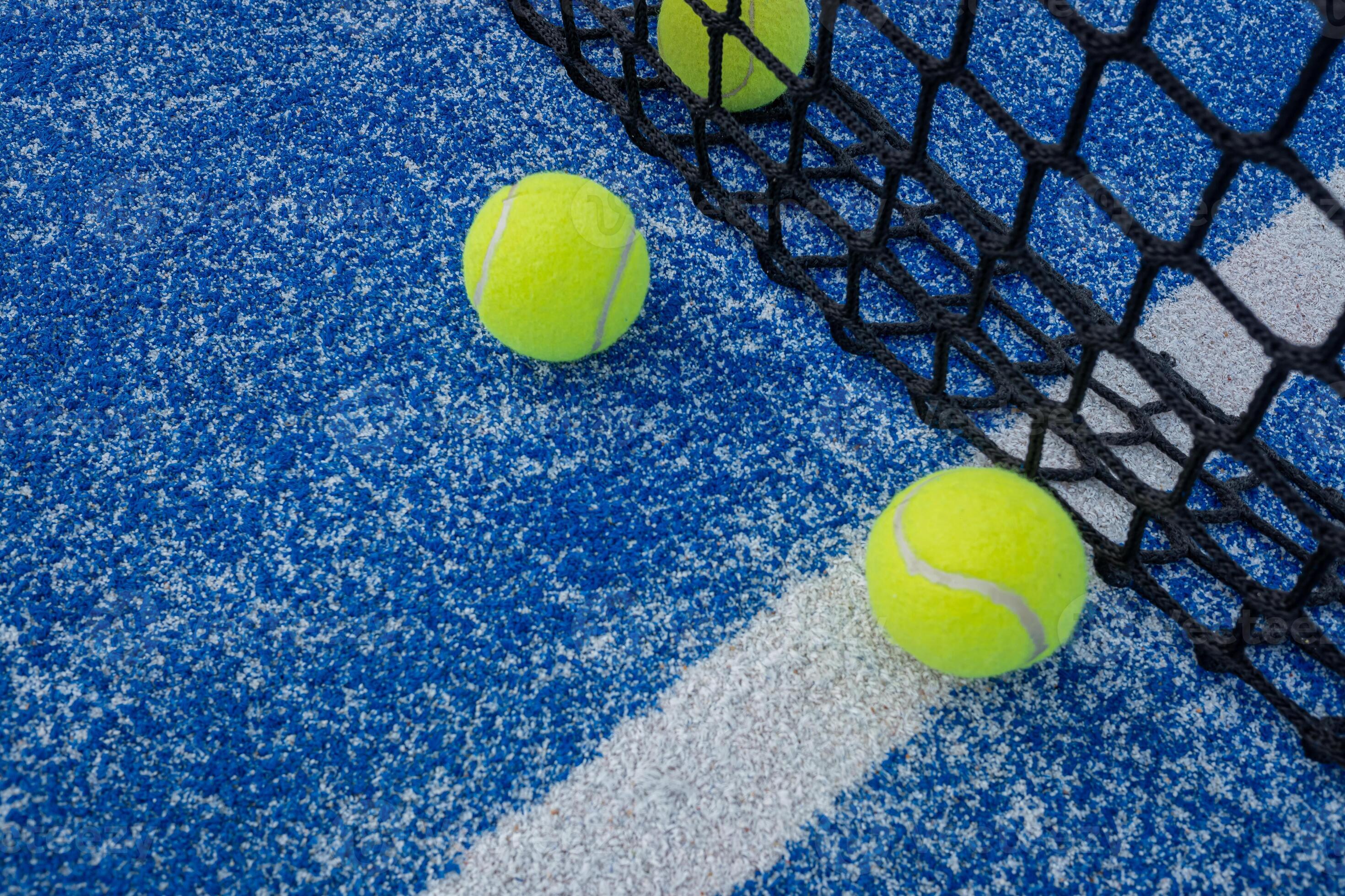 Three yellow balls on floor in front and behind of paddle net in blue court outdoors. Padel ...