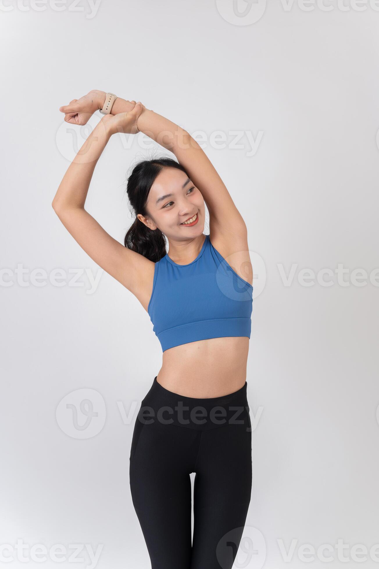 A beautiful, healthy Asian woman in sportswear stretching her arms and body, studio background ...