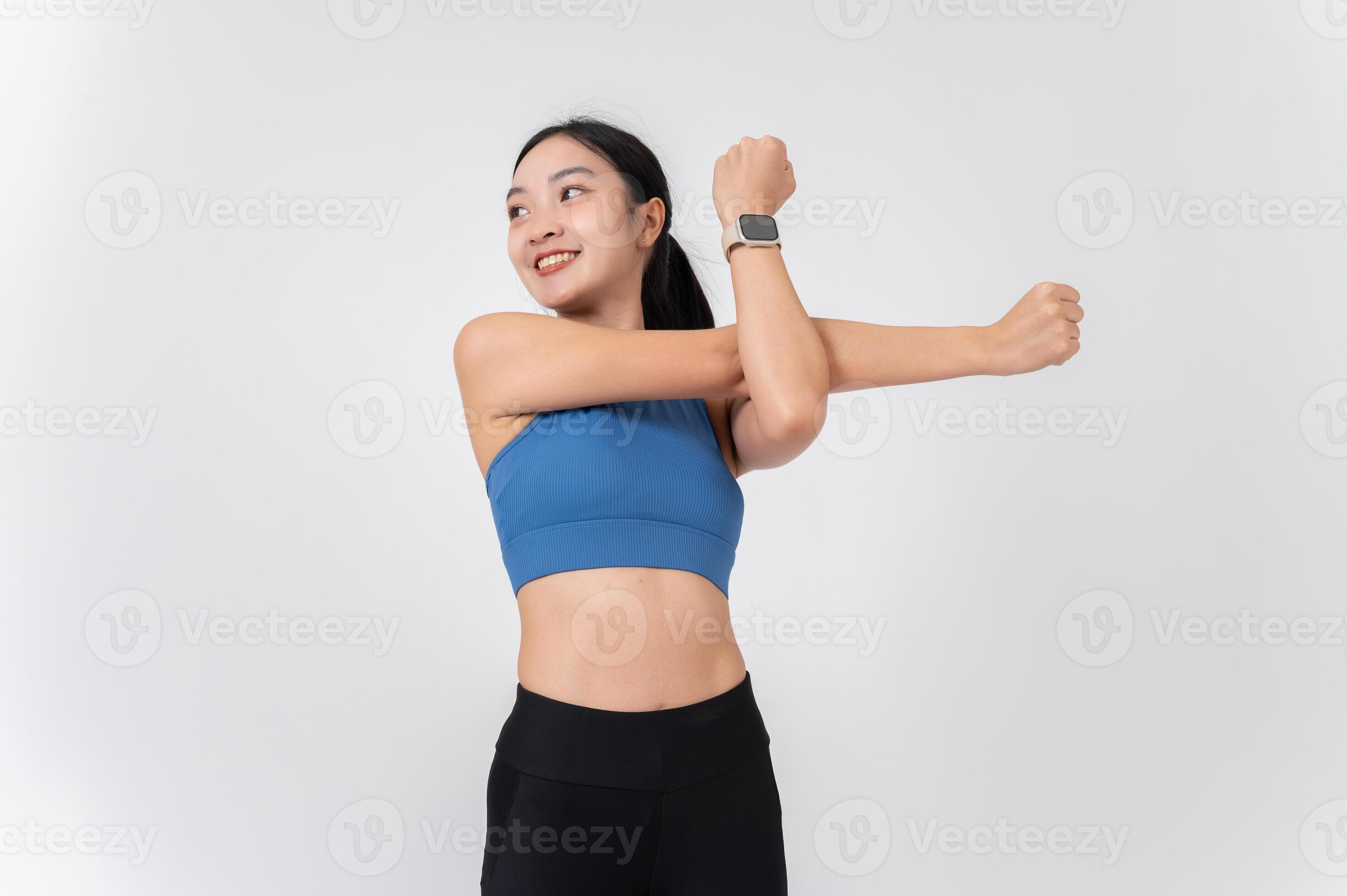 A beautiful, healthy Asian woman in sportswear stretching her arms and body, studio background ...