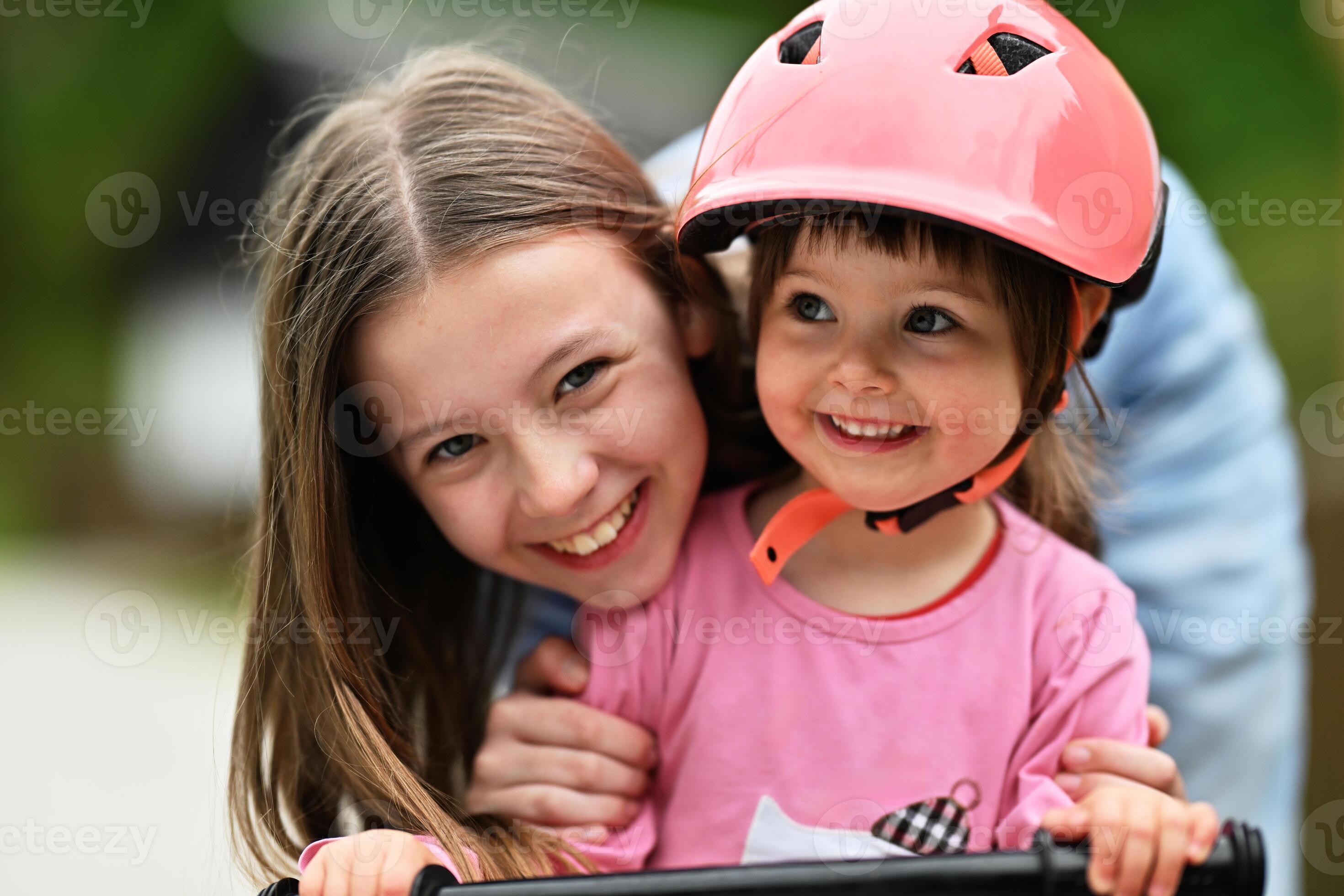 A close up of a teenage girl warmly hugging a young girl wearing a protective helmet while ...