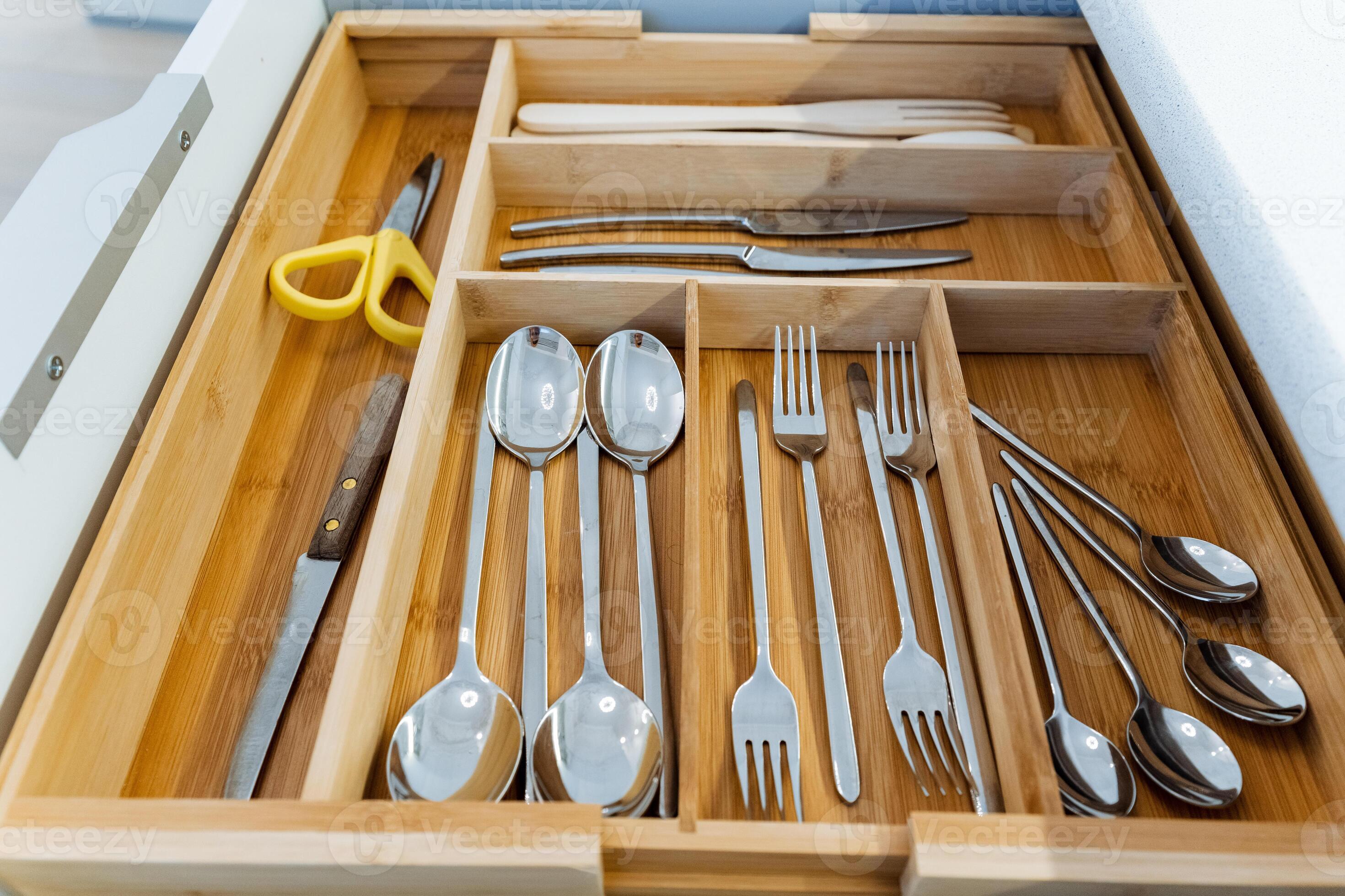 A kitchen drawer is wellorganized with cutlery and utensils in a wooden ...