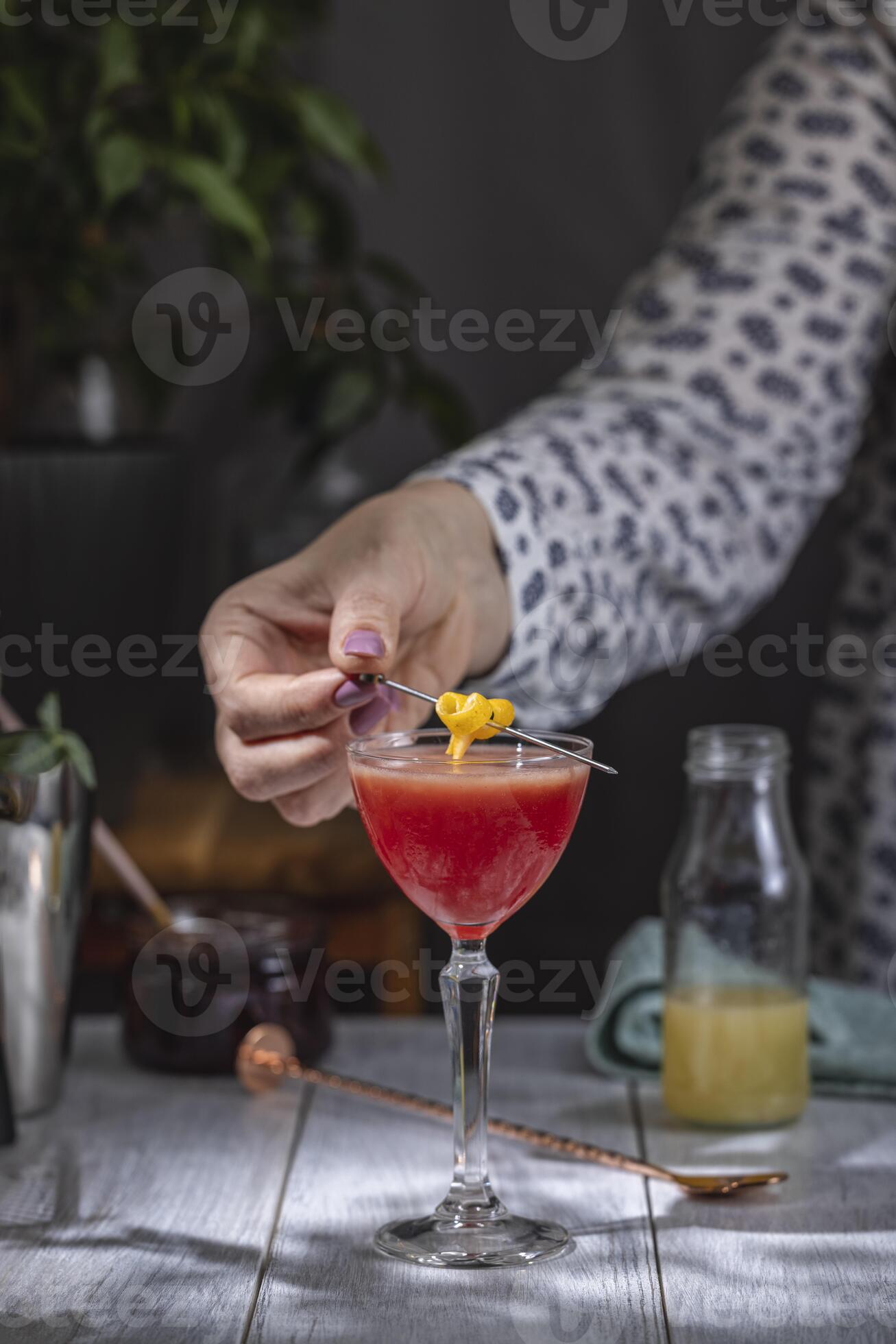 Bartender garnishing red cocktail with lemon twist in coupe glass 54966273 Stock Photo at Vecteezy