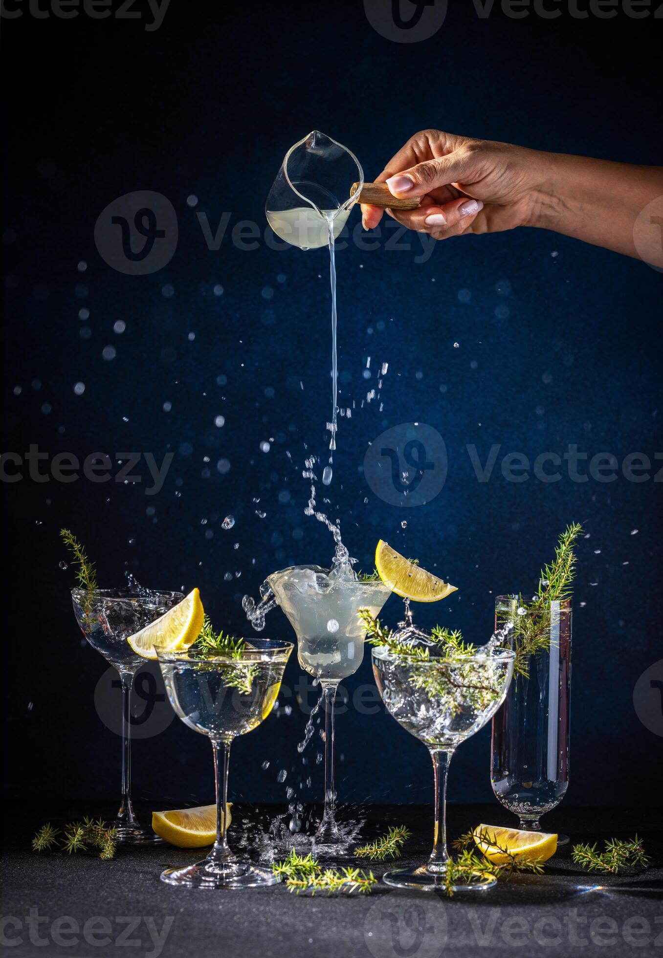 Bartender pouring gin into cocktail glasses with lemon and juniper berries, creating splashing ...