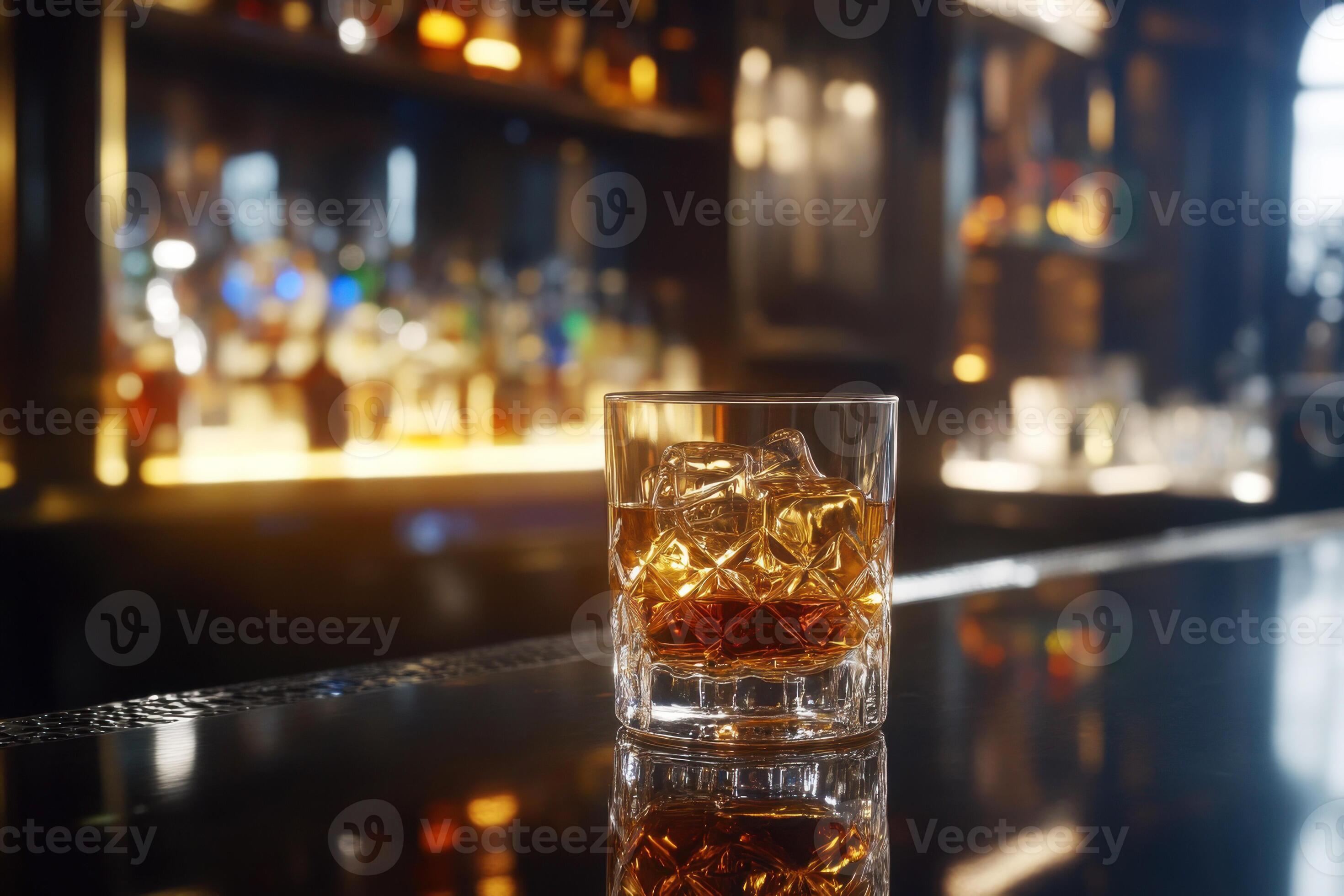 Elegant whiskey glass filled with ice sits on a polished bar counter in a dimly lit lounge ...