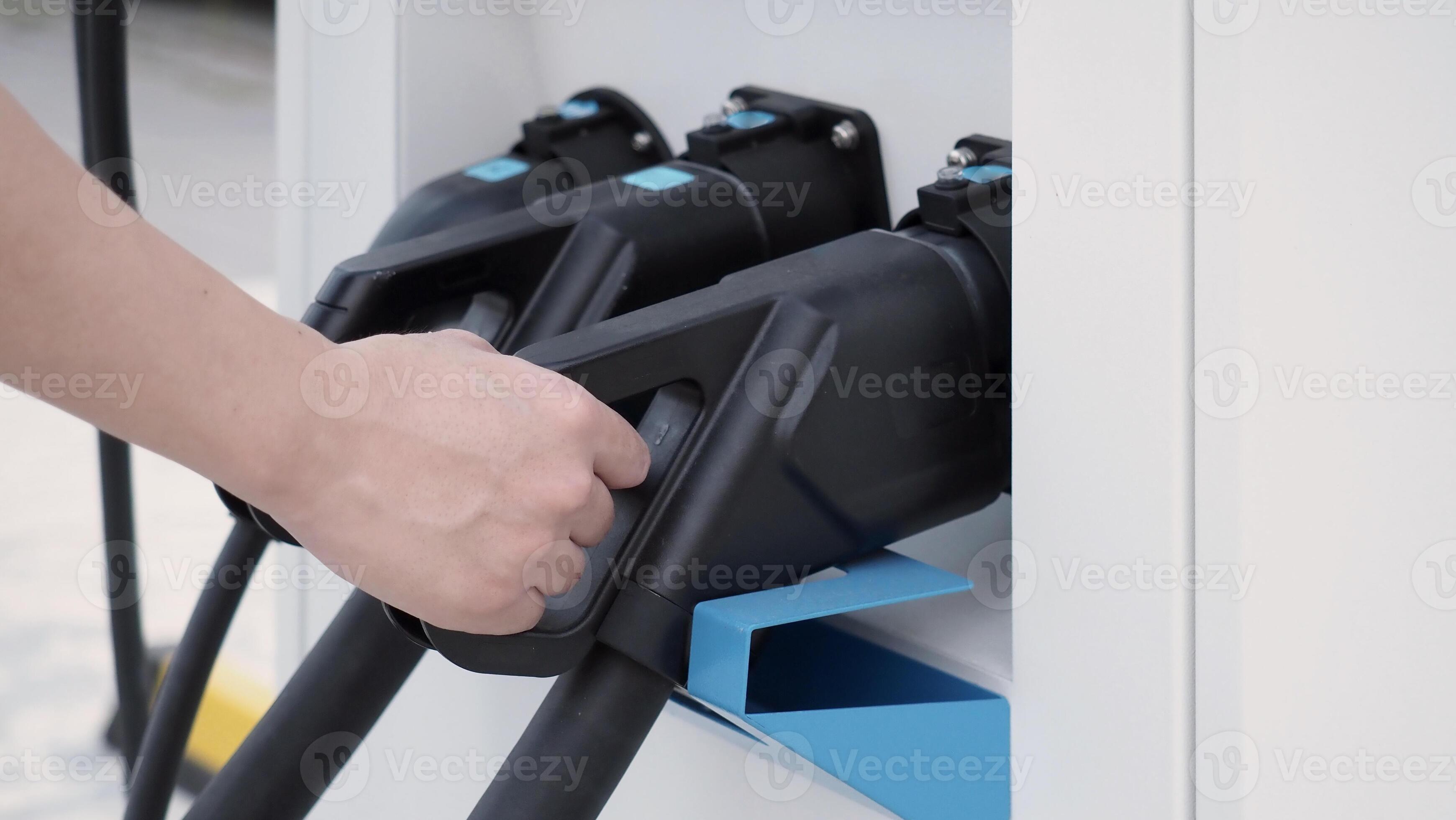 Hand hold EV charging plug in front of camera with blurred background of outdoor. Driver of ...
