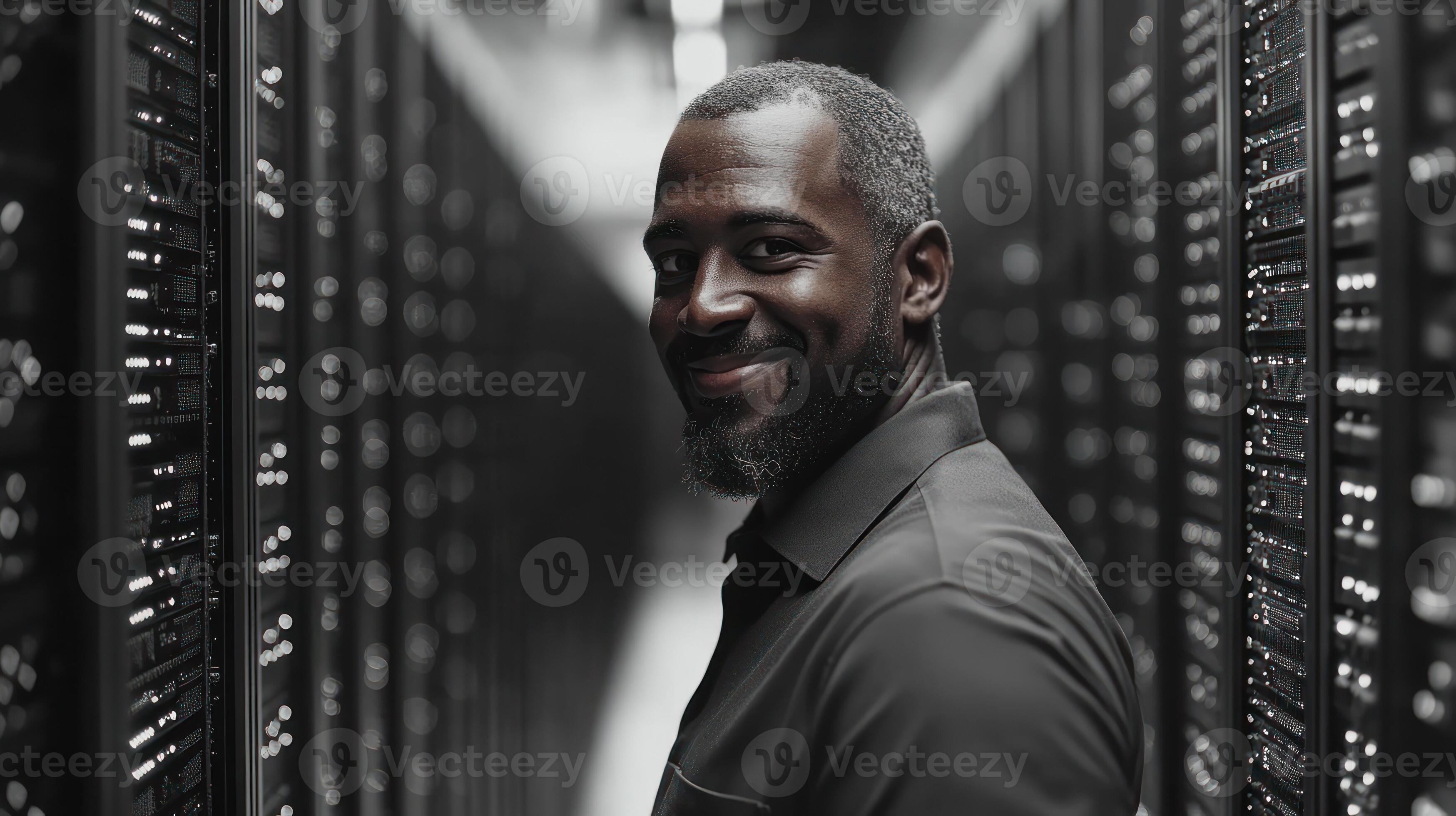 A man stands in a dimly lit data center smiling while surrounded by ...