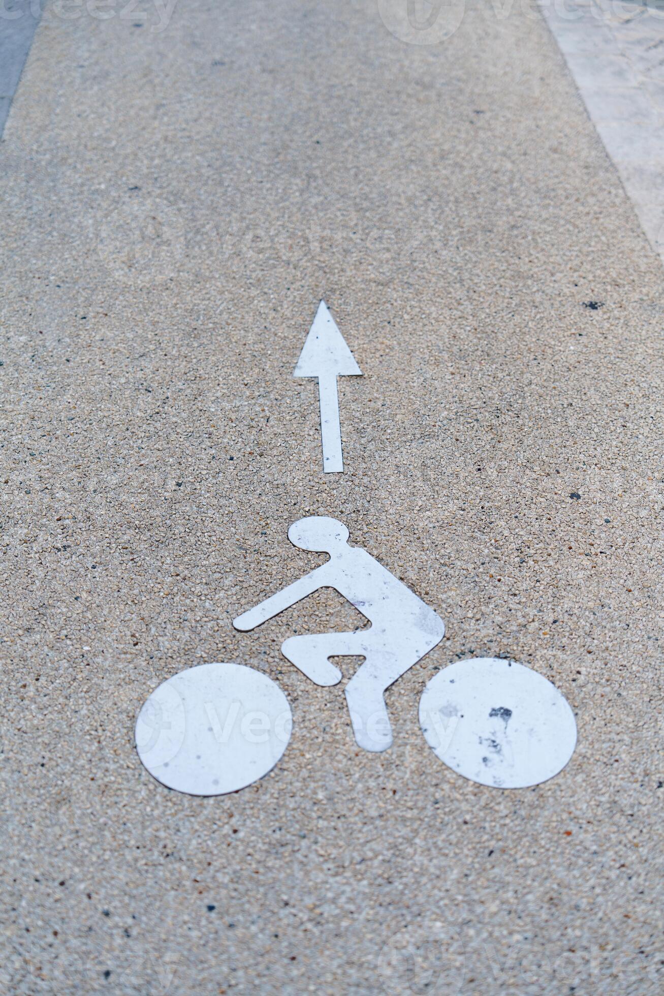 The image displays a white bicycle lane sign on gray concrete. This sign marks the designated ...
