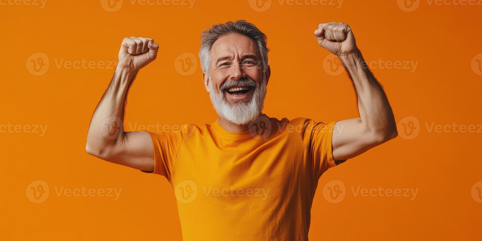 Happy older man celebrating success with raised fists against a vibrant orange background ...