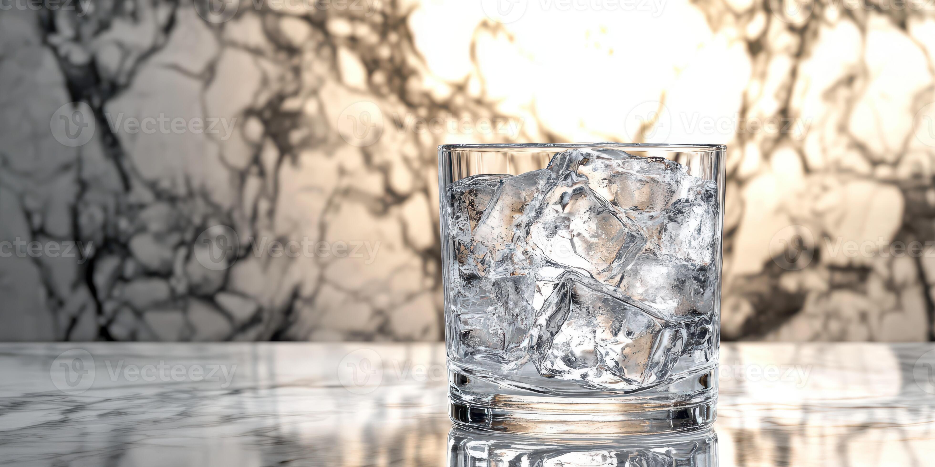 Clear glass filled with ice cubes sits on a polished marble surface reflecting warm light ...