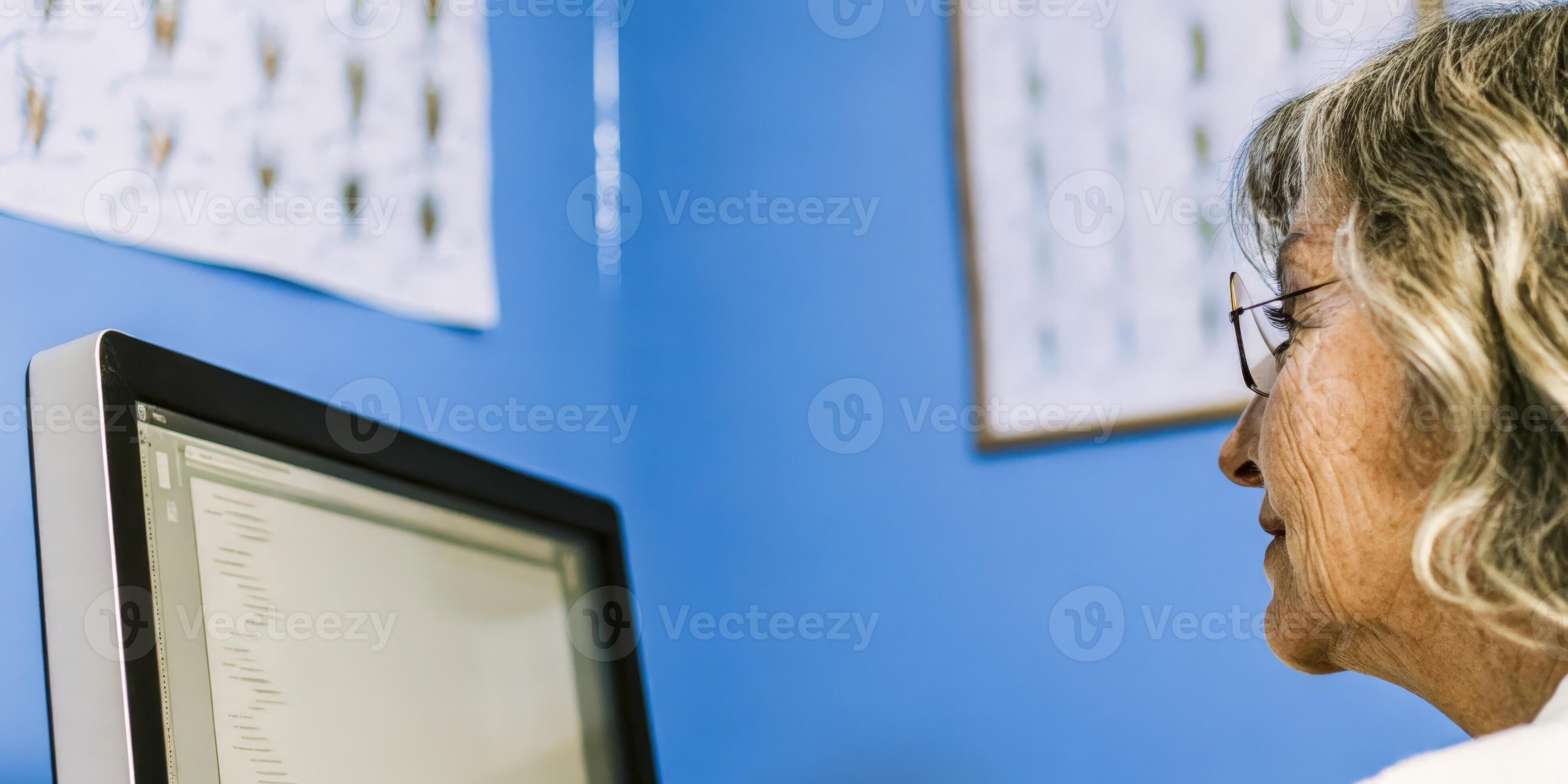 A closeup of a senior womans face illuminated by a computer screen displaying a mixture of ...