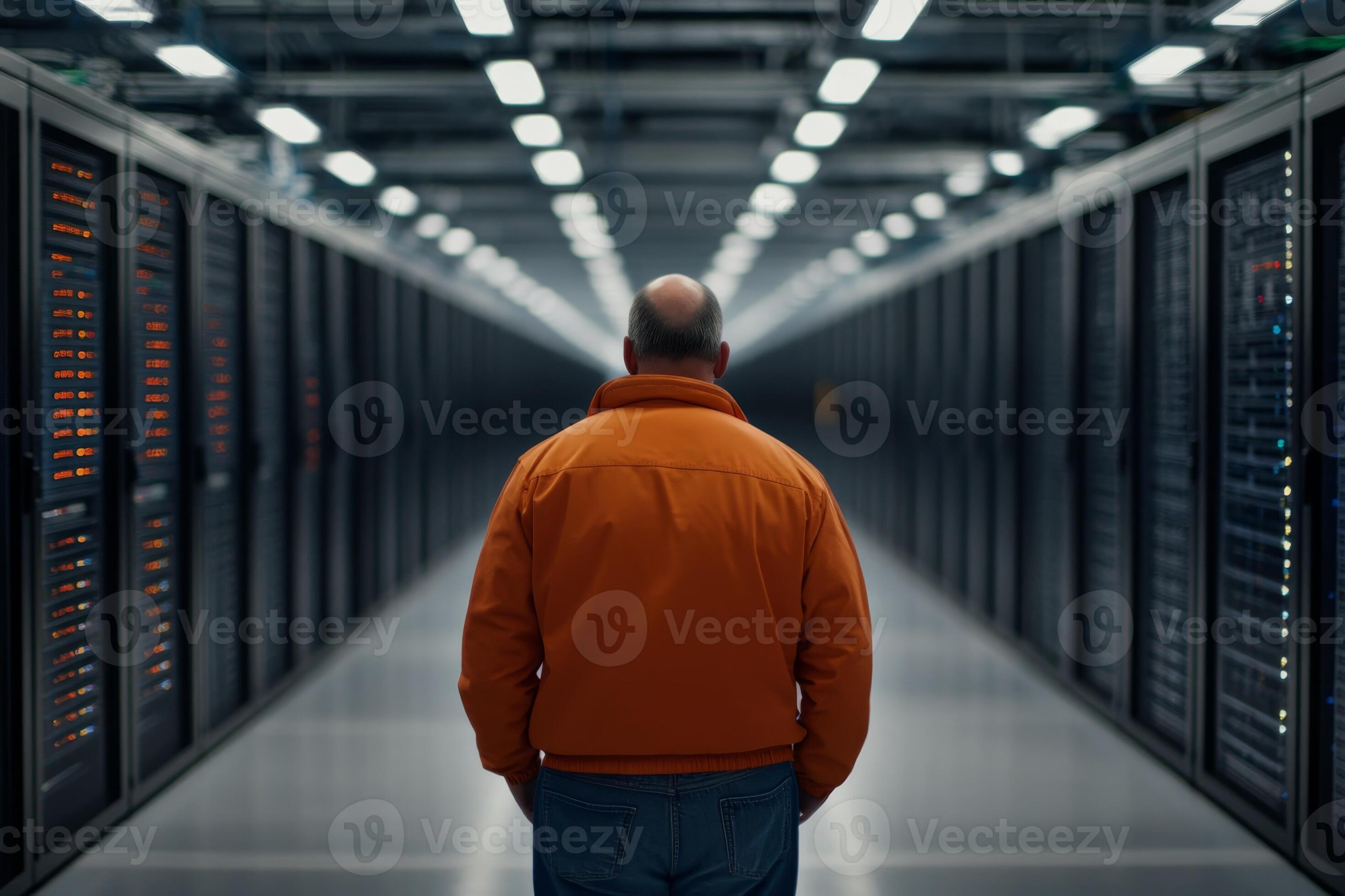 Person in orange jacket walks through data center filled with servers in a dimly lit corridor ...