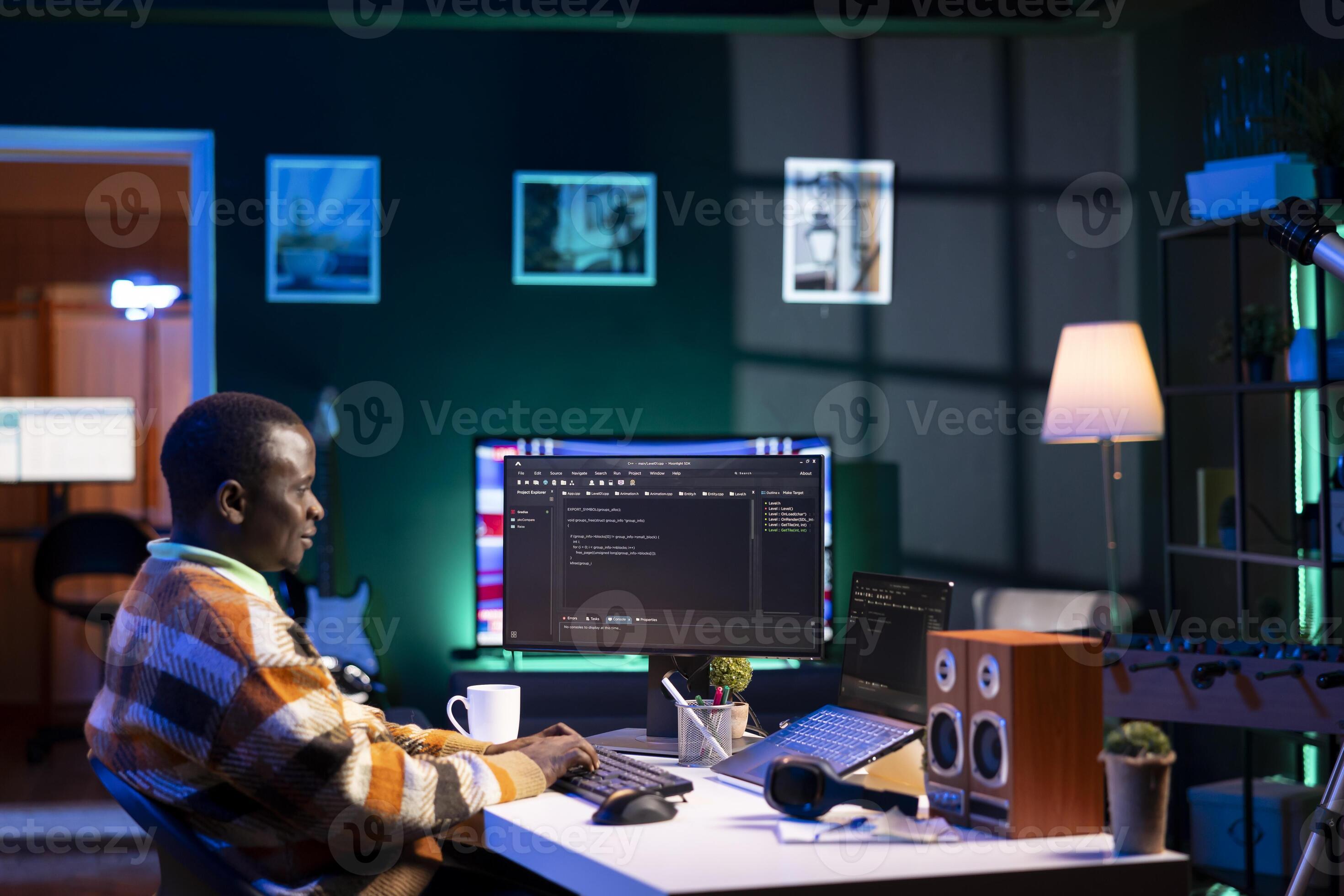 Programmer in home office concentrating on finding bugs while he codes on his computer. African ...