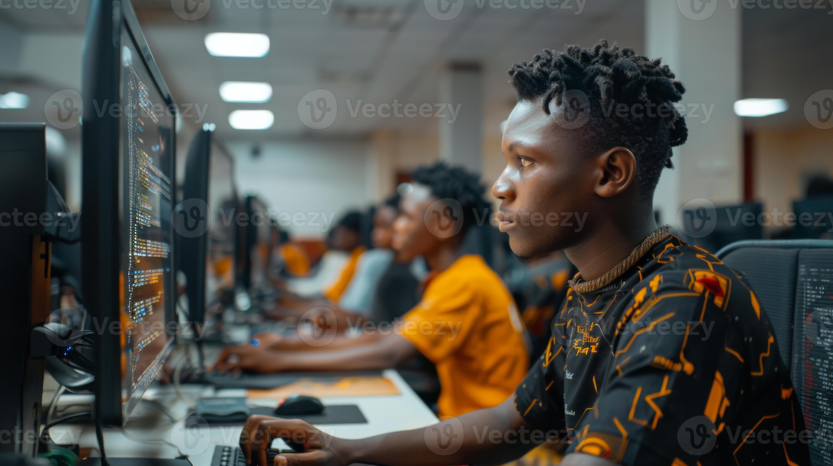 A group of young students focuses intently on computer screens ...