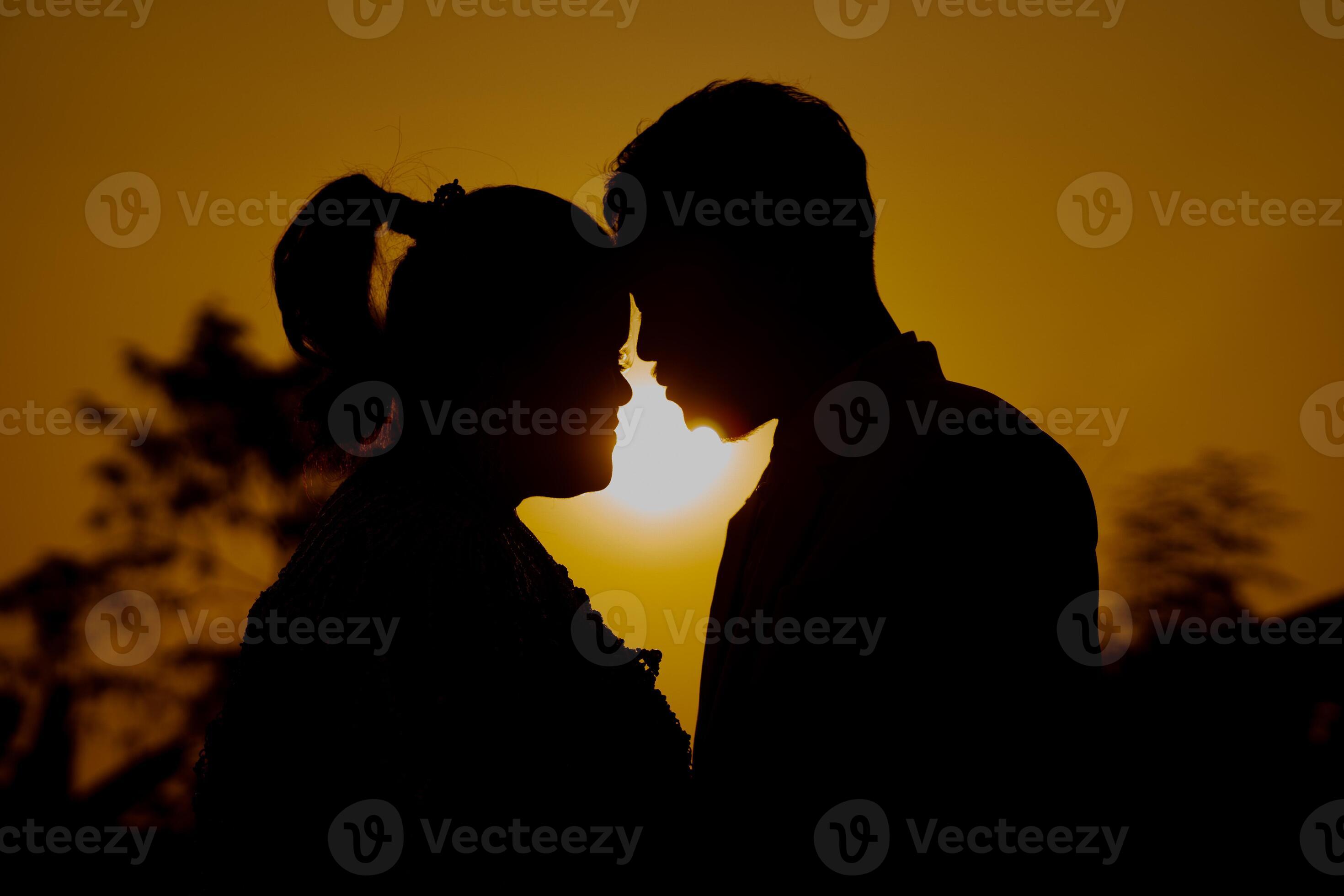 Romantic silhouette of a couple at sunset, man kissing woman's forehead, love and intimacy ...