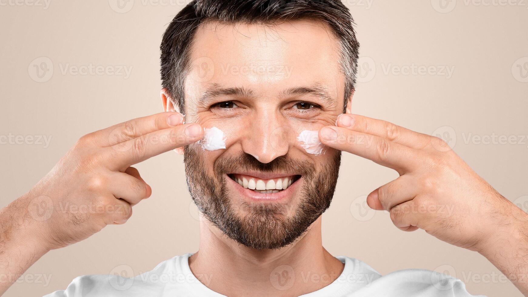 Smiling handsome man applying anti-aging cream on his face, closeup ...