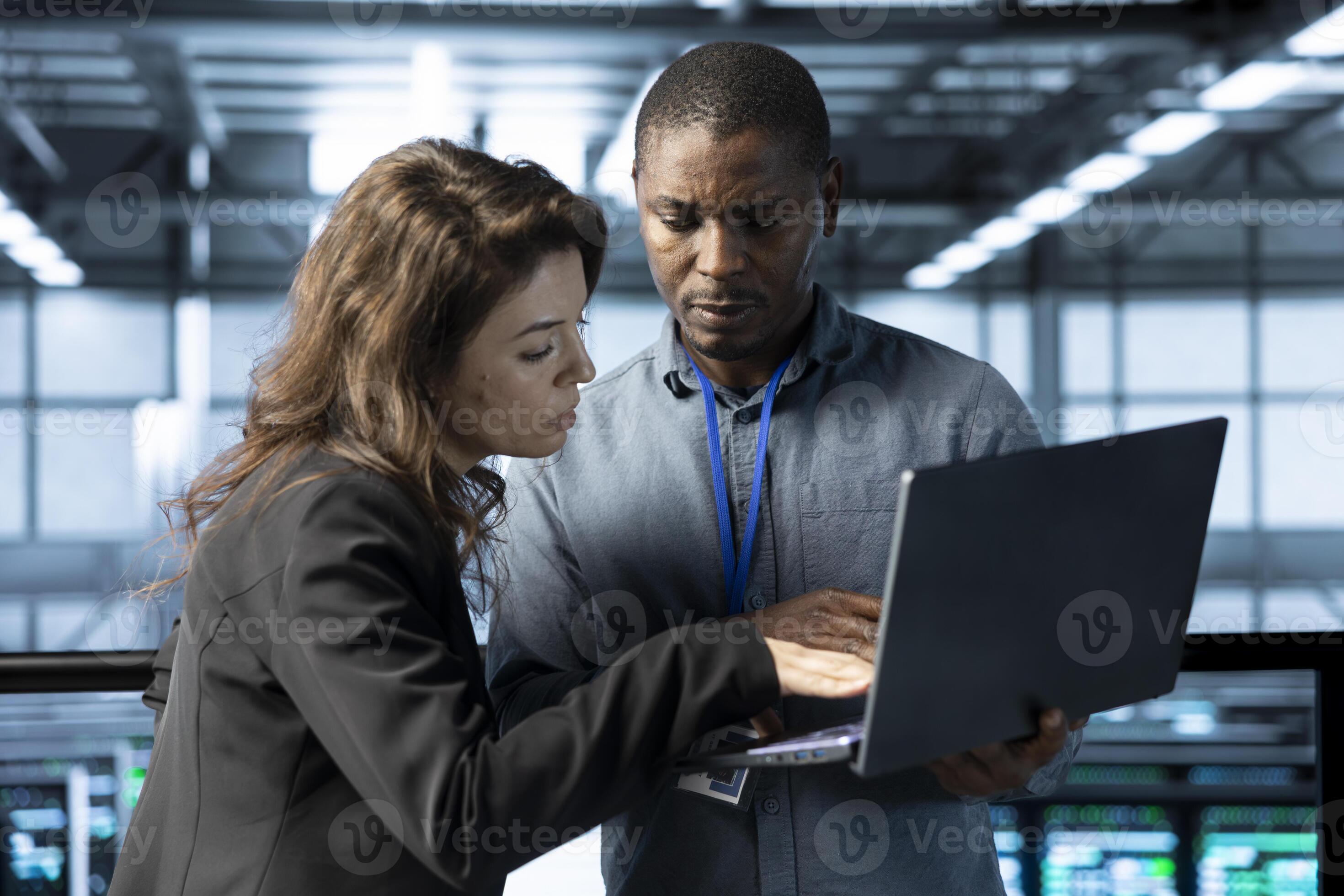 System administrators in data center automating routine maintenance tasks with laptop, executing ...