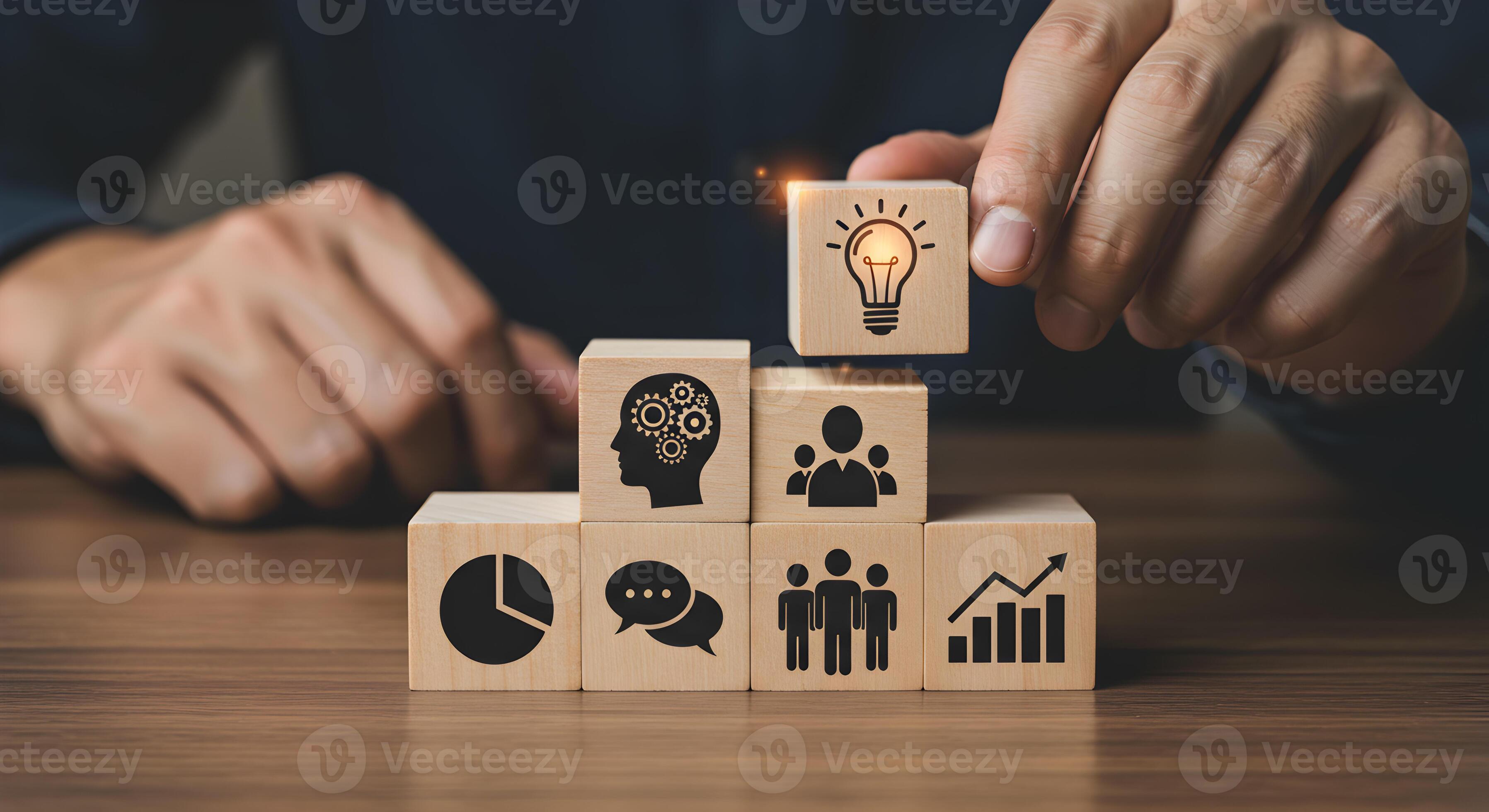 Person placing wooden block with lightbulb icon on top of a stack of ...