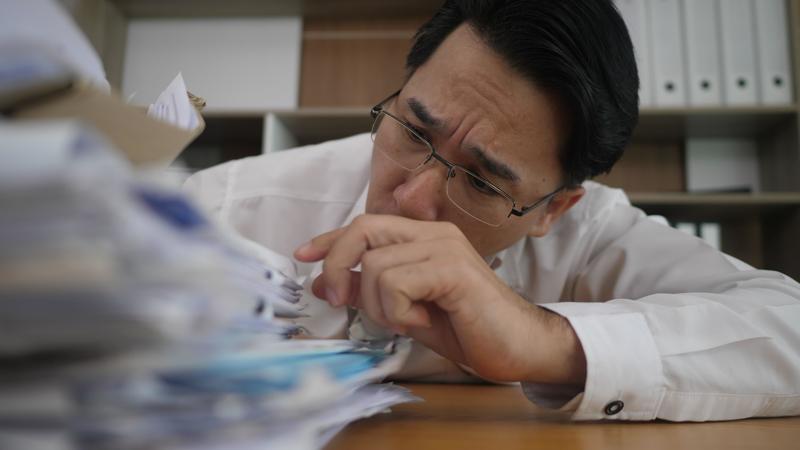 Overworked businessman looking at a stack of paper documents in hid ... Overworked businessman looking at a stack of paper documents in hid ...