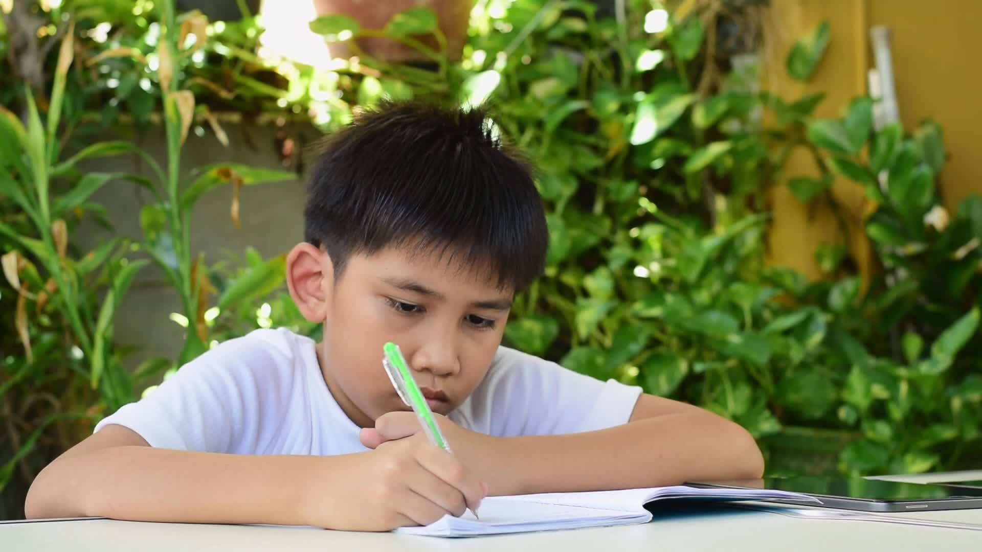 Asian Boy Doing His Homework Using A Pen To Write On A Notebook asian-boy-doing-his-homework-using-a-pen-to-write-on-a-notebook