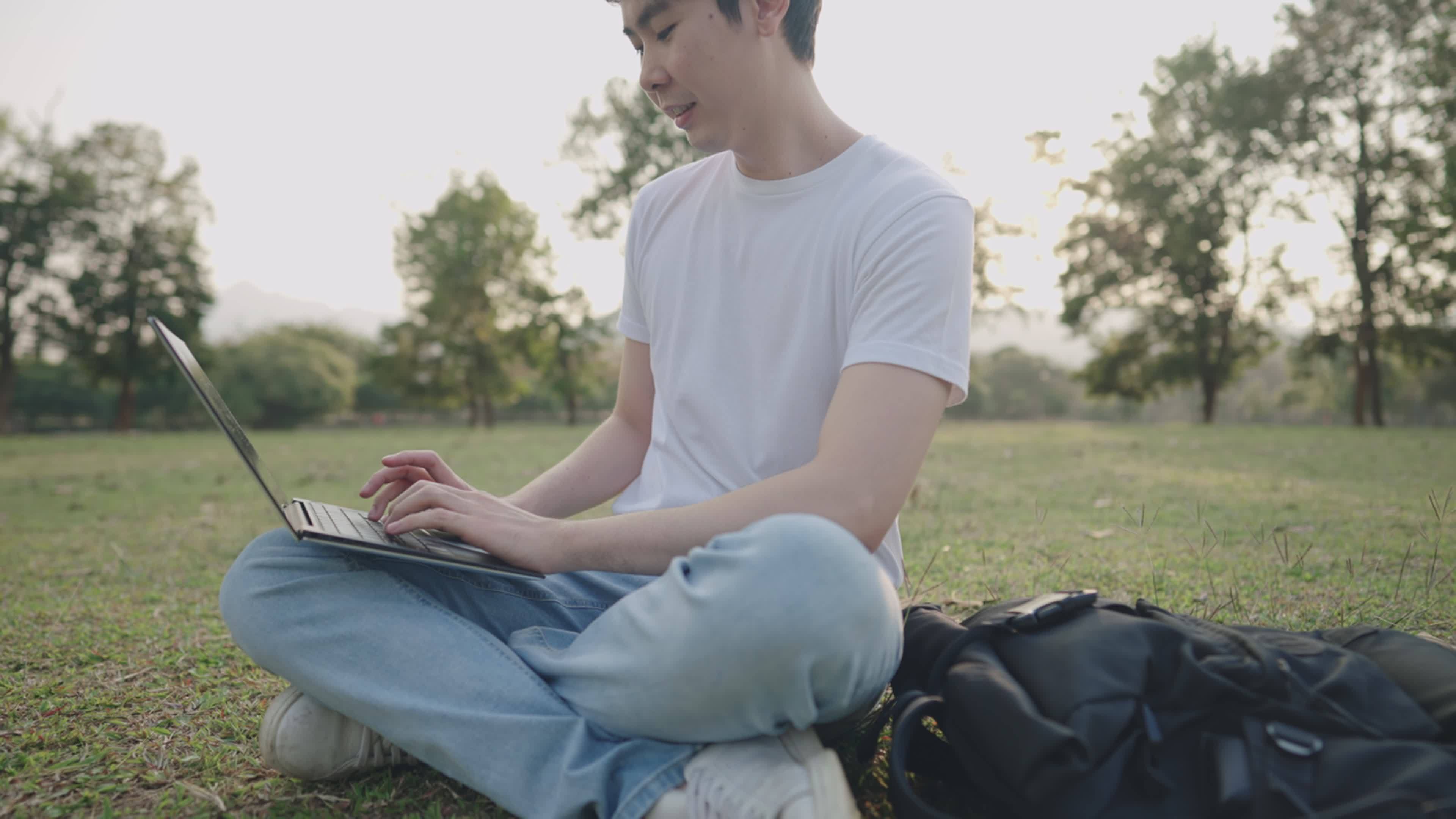Young attractive asian man working with laptop in green park during a ...