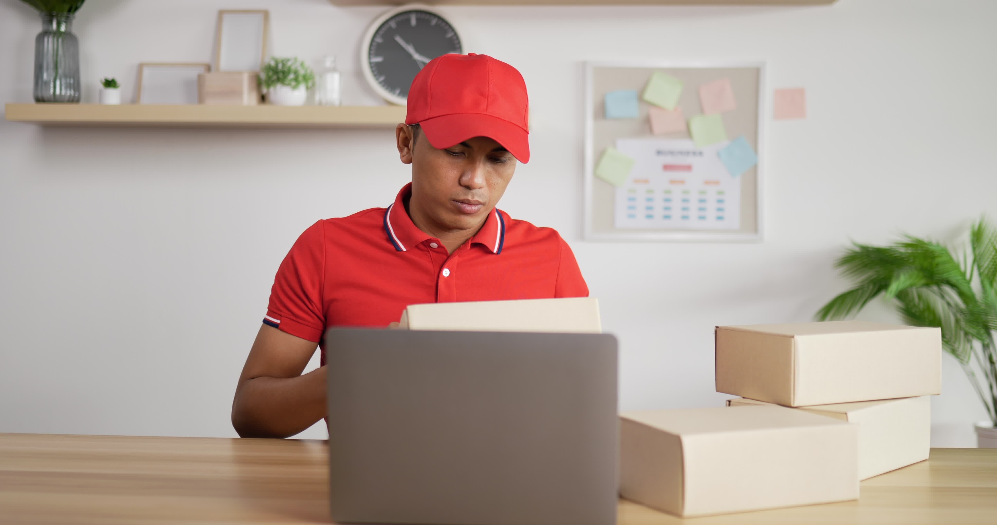 Portrait of Young Asian postman in red uniform and cap sitting at desk ...