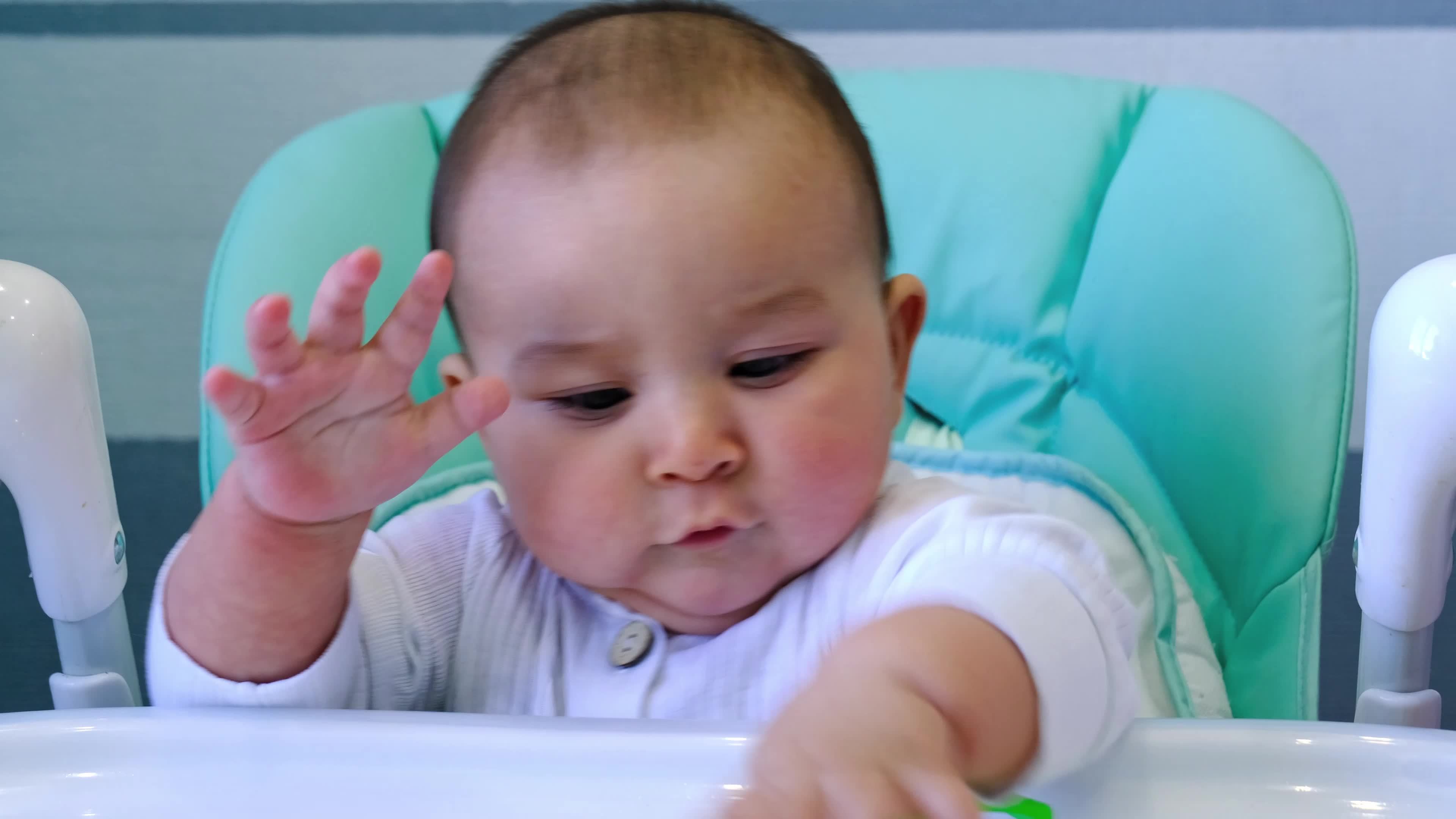 A Hungry Baby Is Gnawing On A Plastic Spoon At The Table On A High a-hungry-baby-is-gnawing-on-a-plastic-spoon-at-the-table-on-a-high