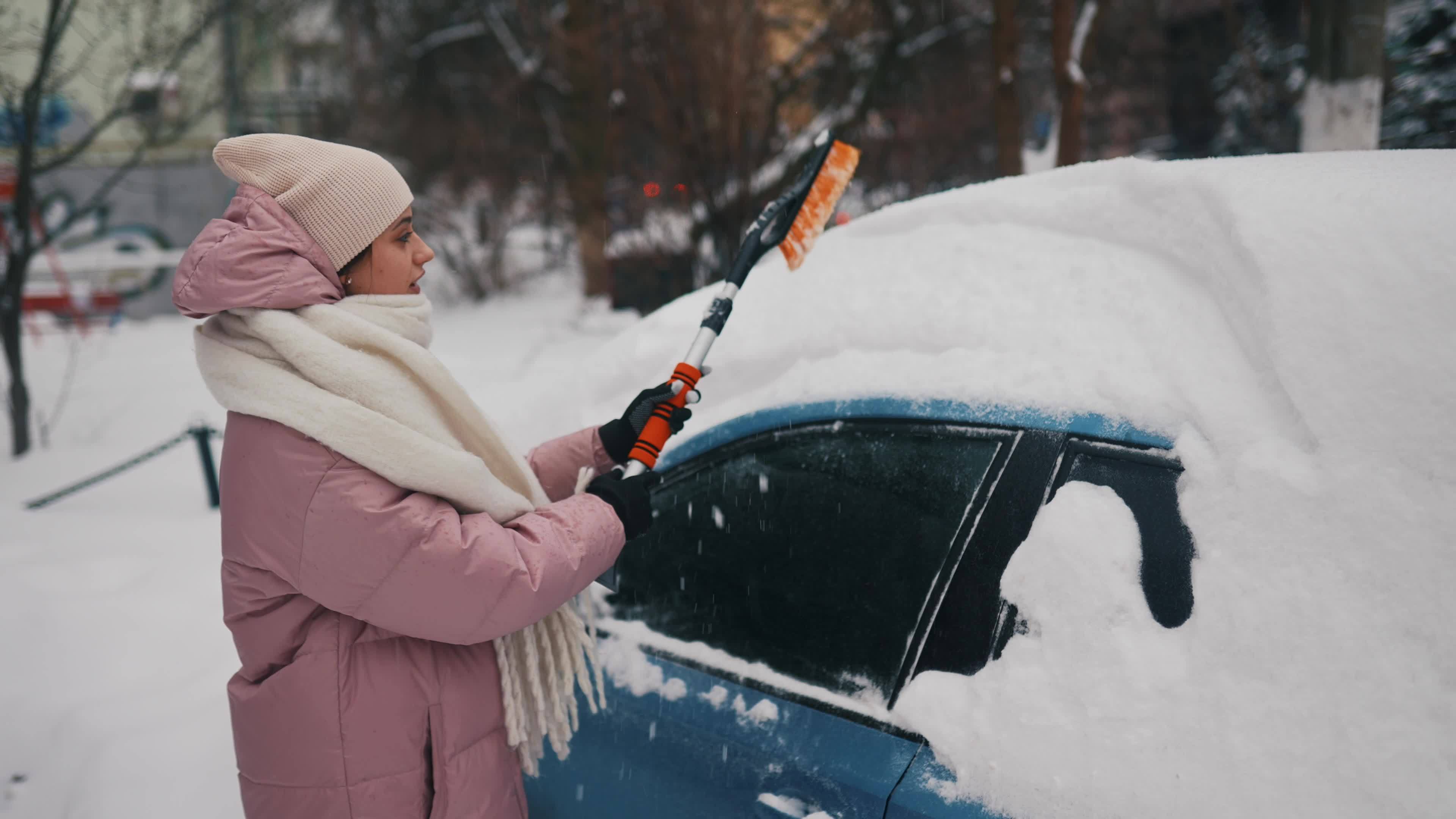 Young woman in pink puffy coat brushes snow off car 11698034 Stock ...