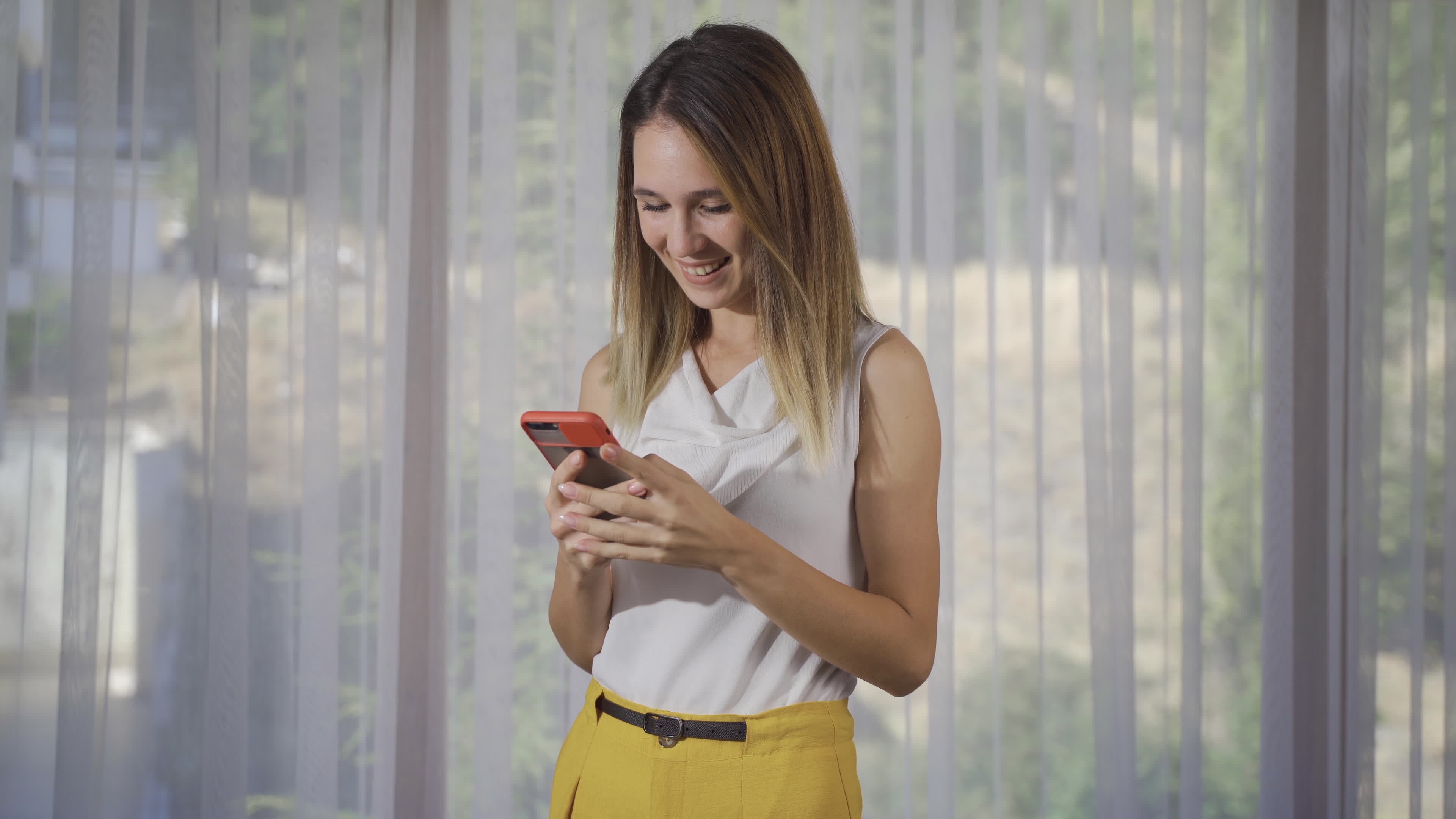 mujer joven regocijándose mirando el teléfono. la mujer que mira el teléfono se regocija y es ...