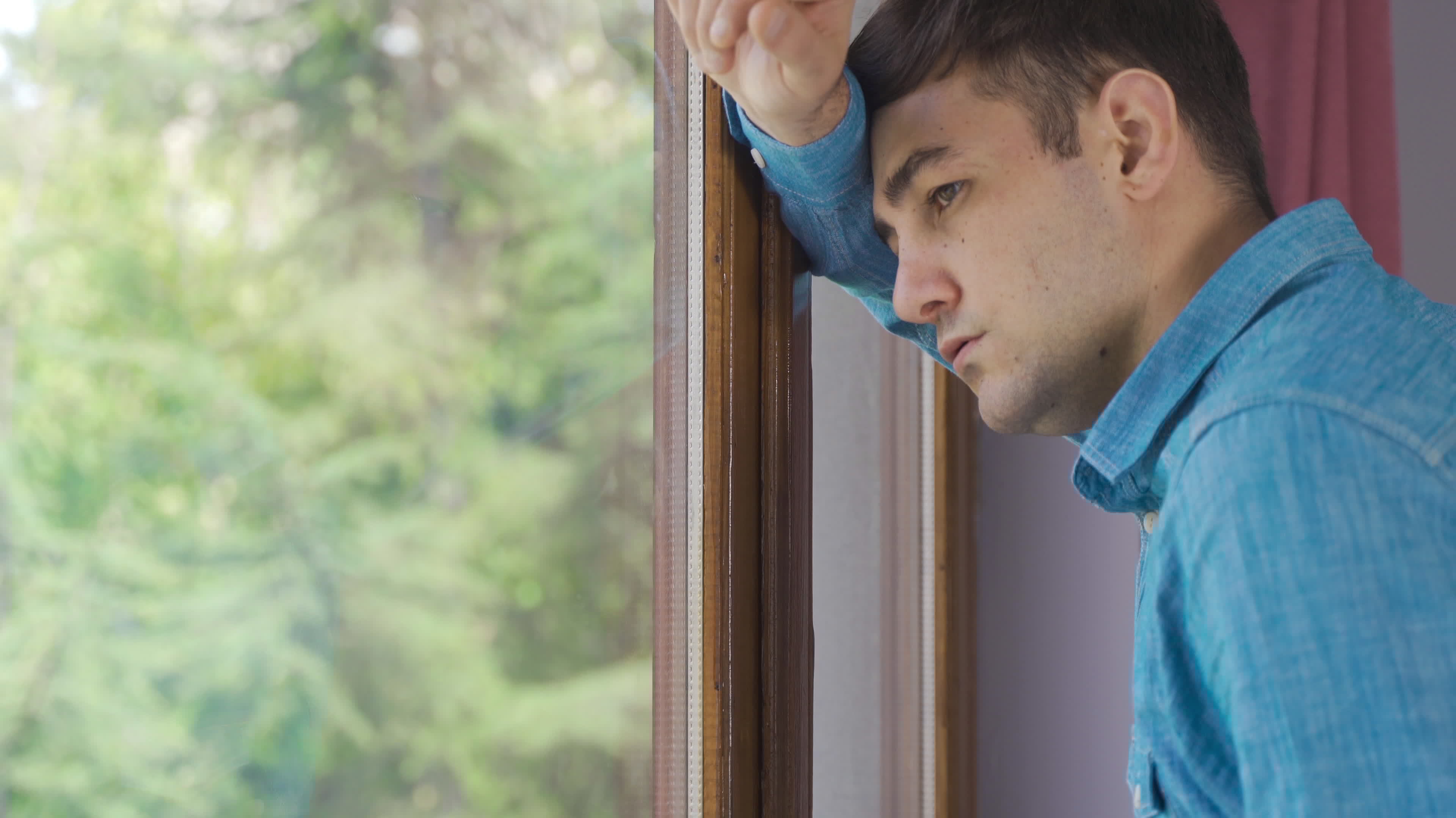 Sad man watching out the window. The man leaning his head against the window looks sadly out the ...