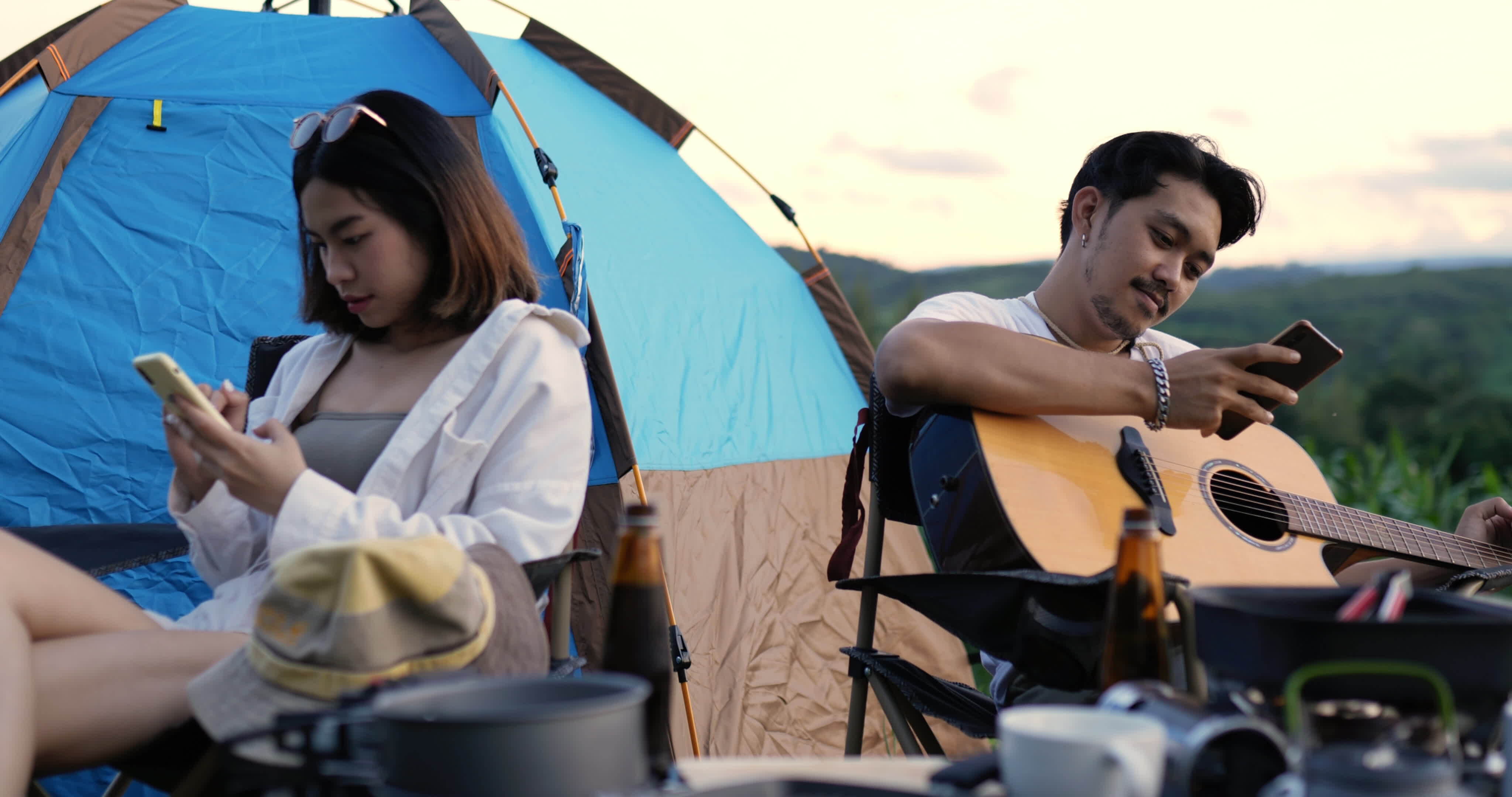 Handheld shot, Young couples use their mobile phones while vacationing together at camping ...