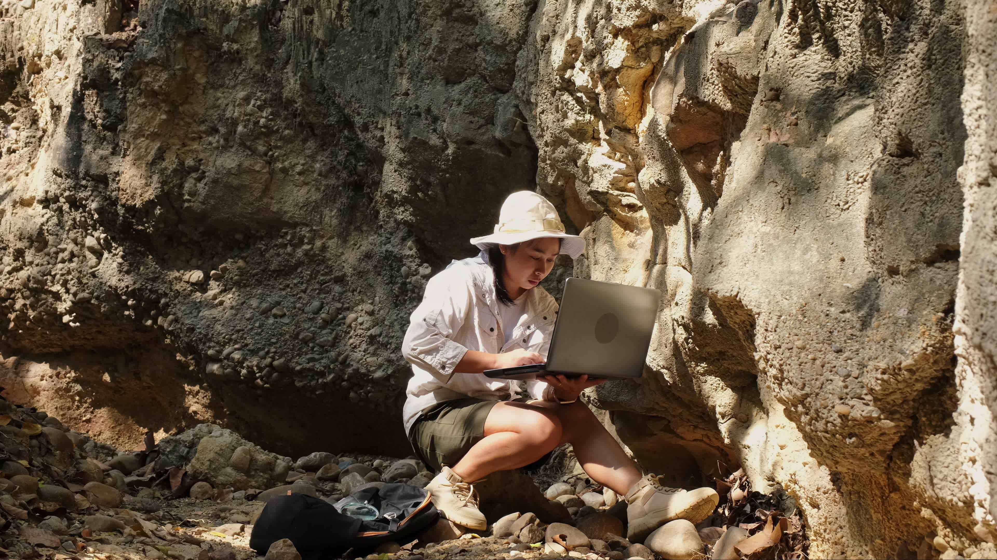 Female geologist using laptop computer examining nature, analyzing rocks or pebbles. Researchers ...