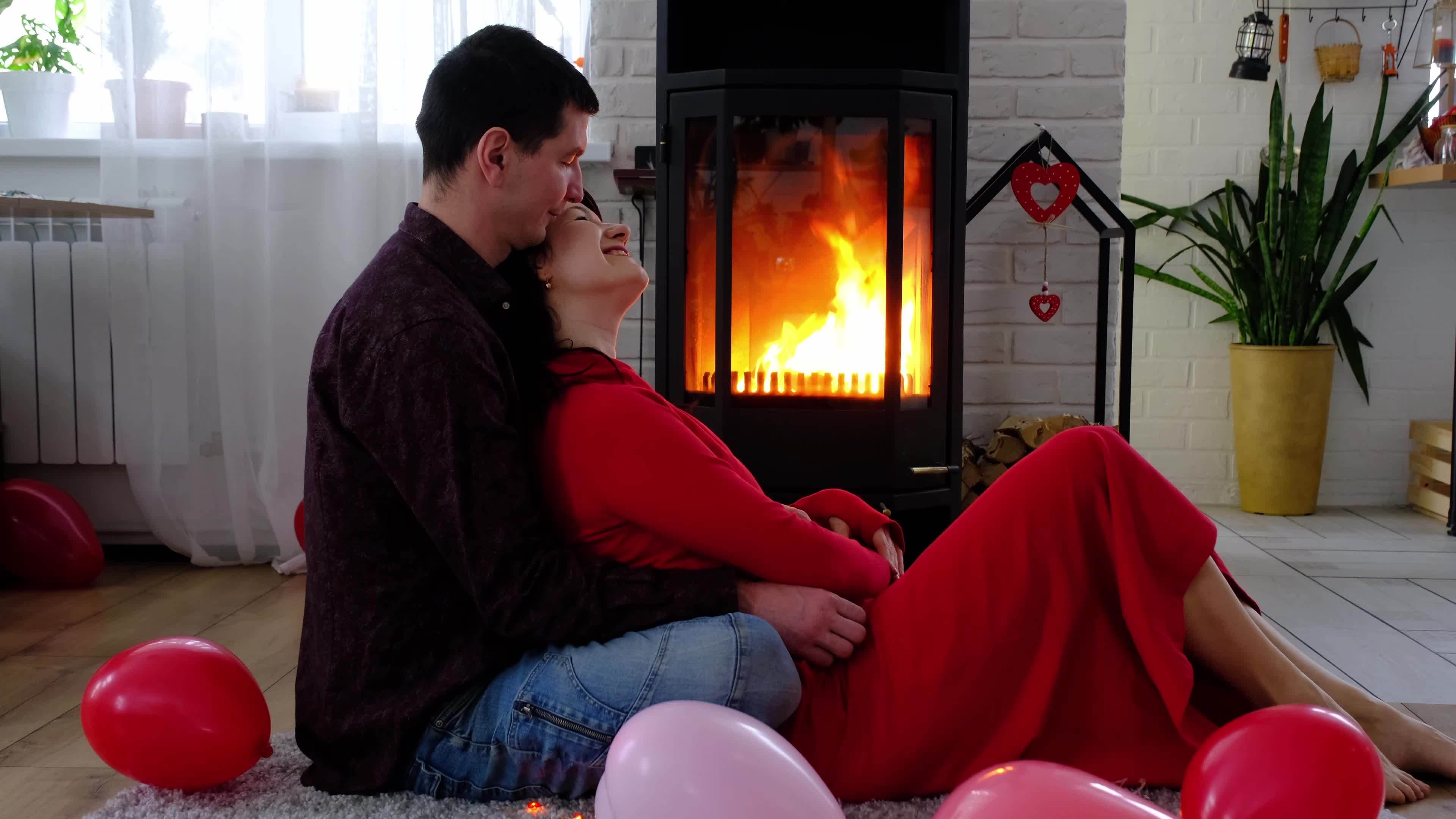 Man and woman in love date at home are sitting near the fireplace stove with a burning fire on a ...