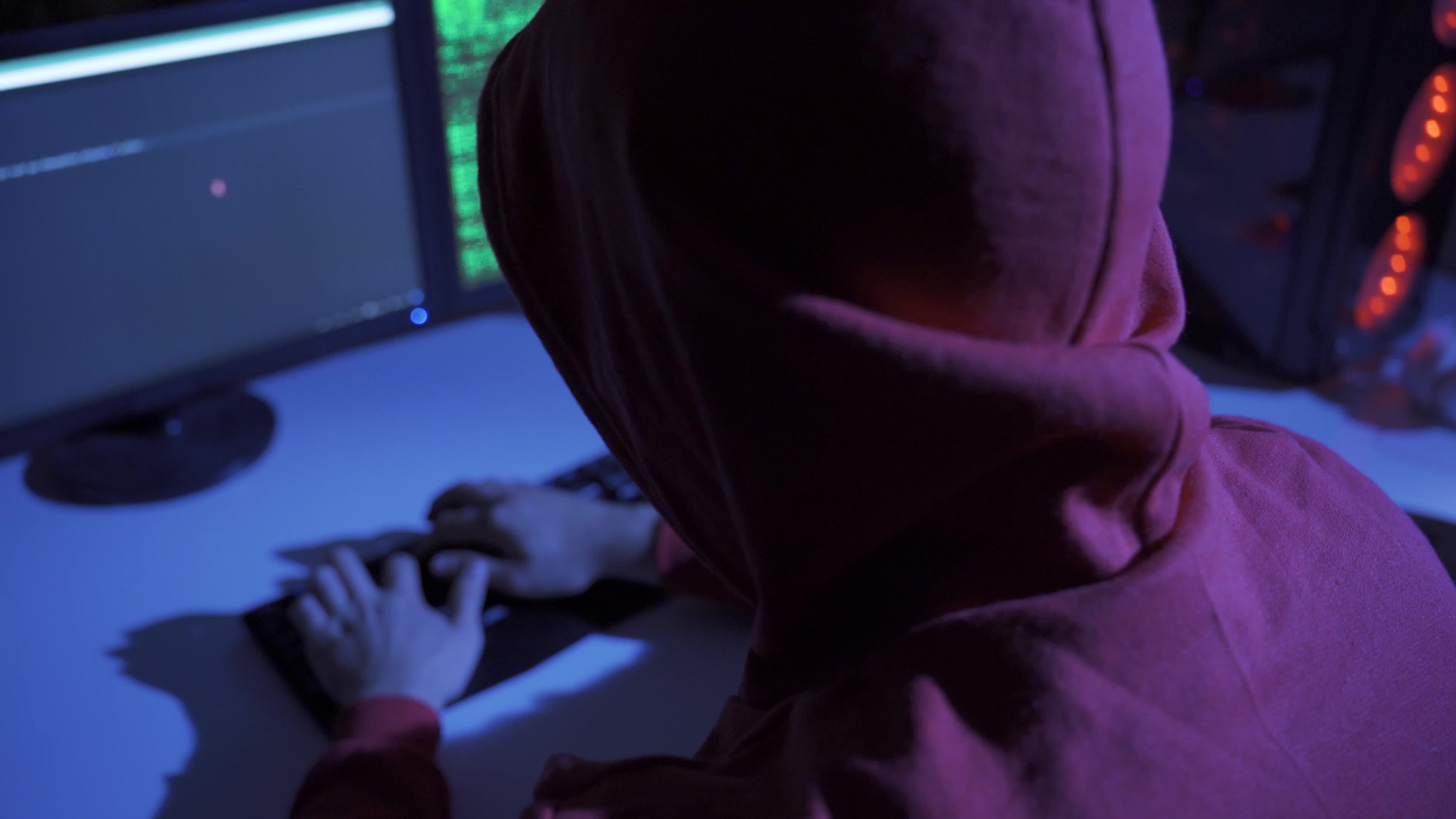 Hacker. Side view of hacker sitting near computer monitors with green ...